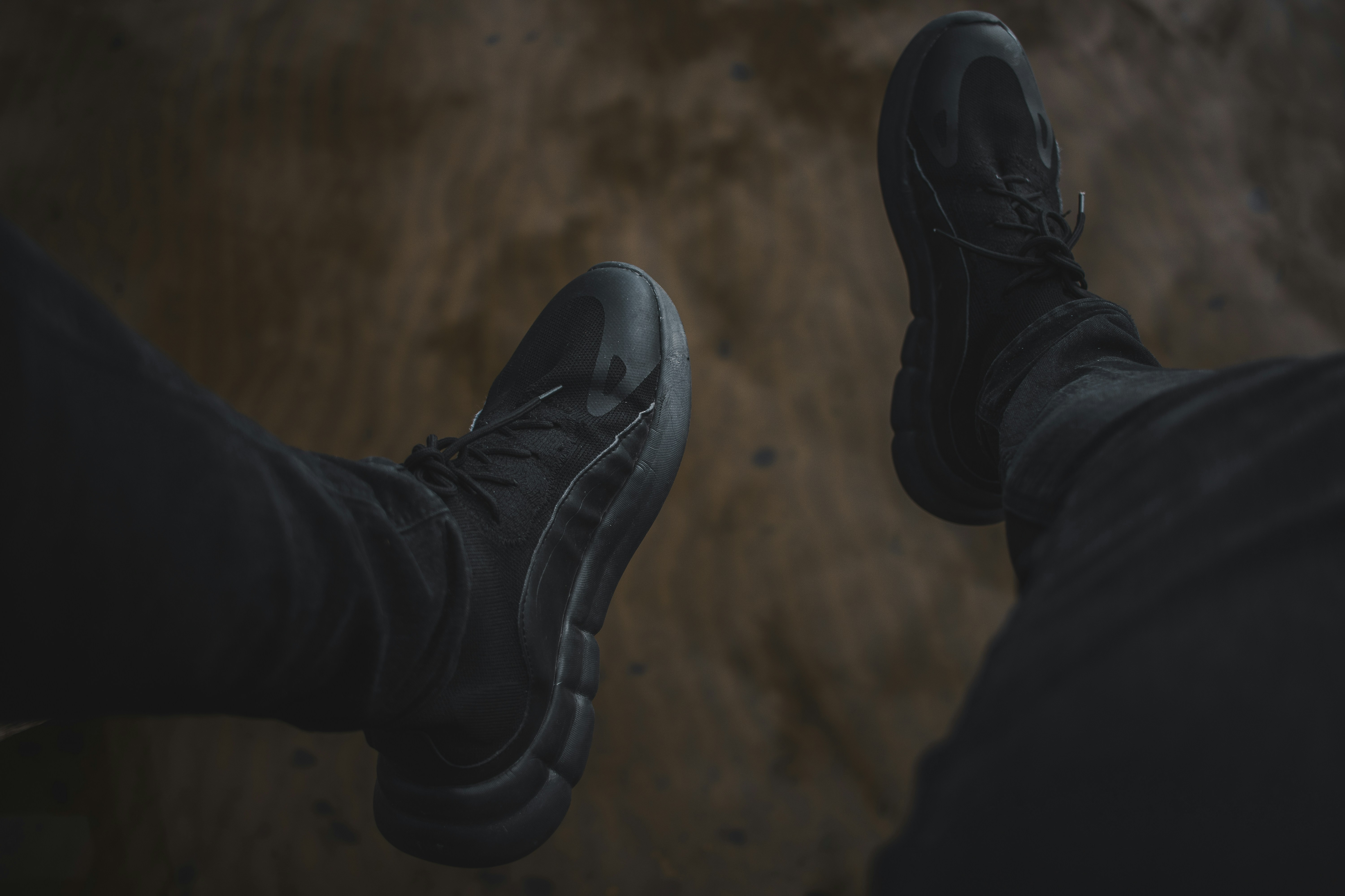 Close-up of black sneakers worn with dark jeans, resting on a textured surface. The composition emphasizes urban fashion and casual comfort.