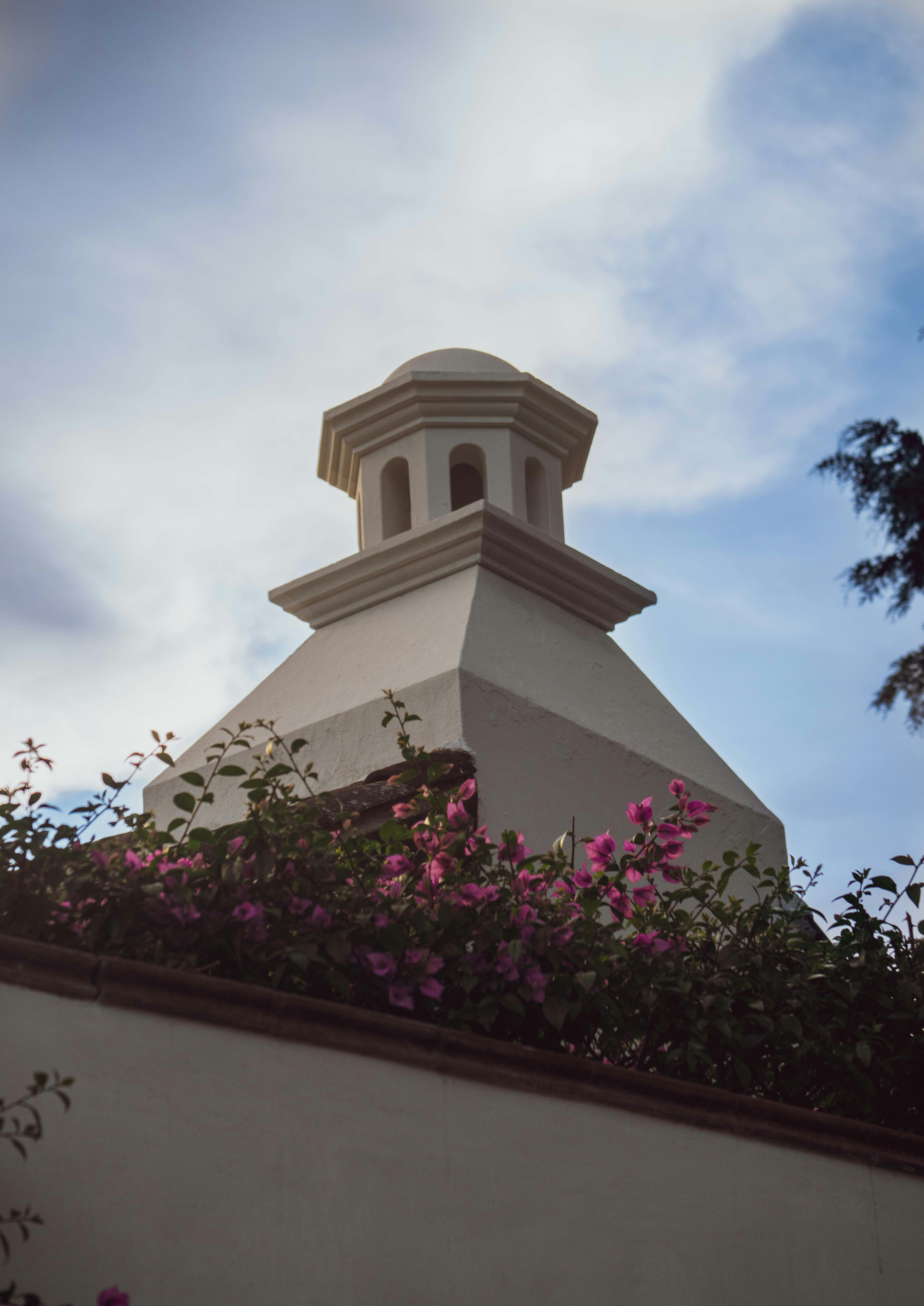 Stylized architectural feature crowned by vibrant bougainvillea blooms against a serene sky.