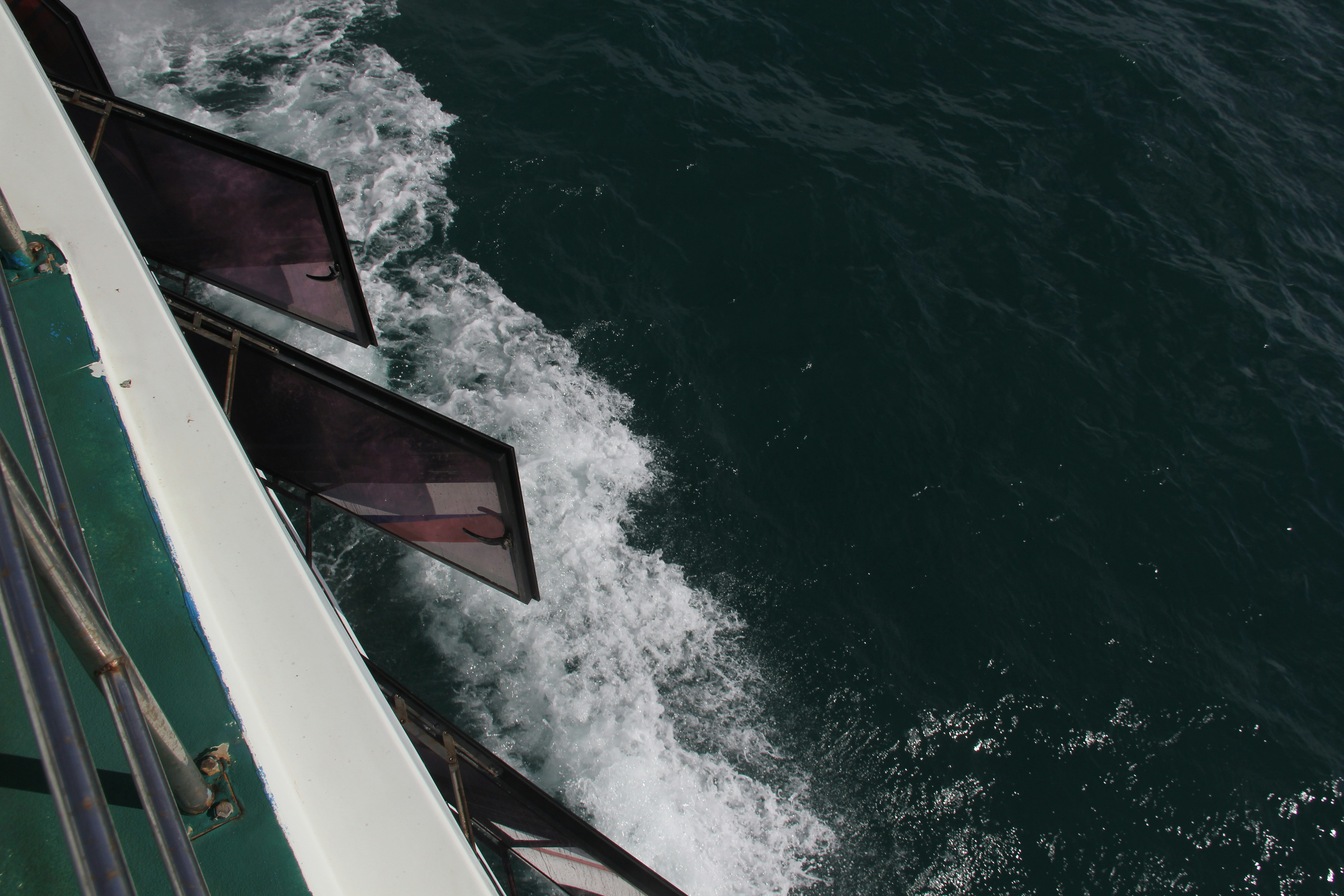 Boat's side with flapping sails cutting through choppy waves under a clear sky.
