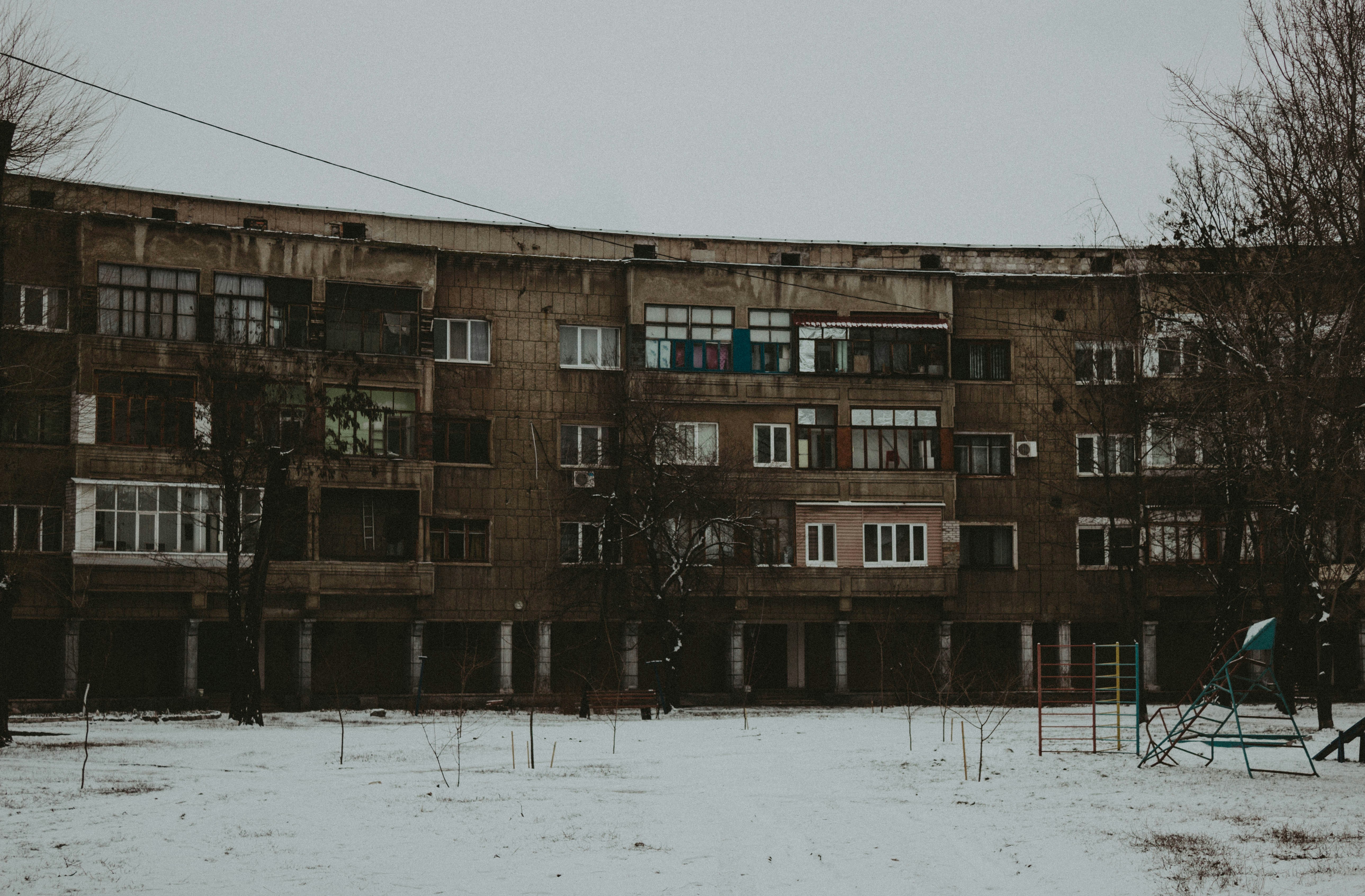 Abandoned apartment building with exposed balconies and a playground, set against a snowy landscape.