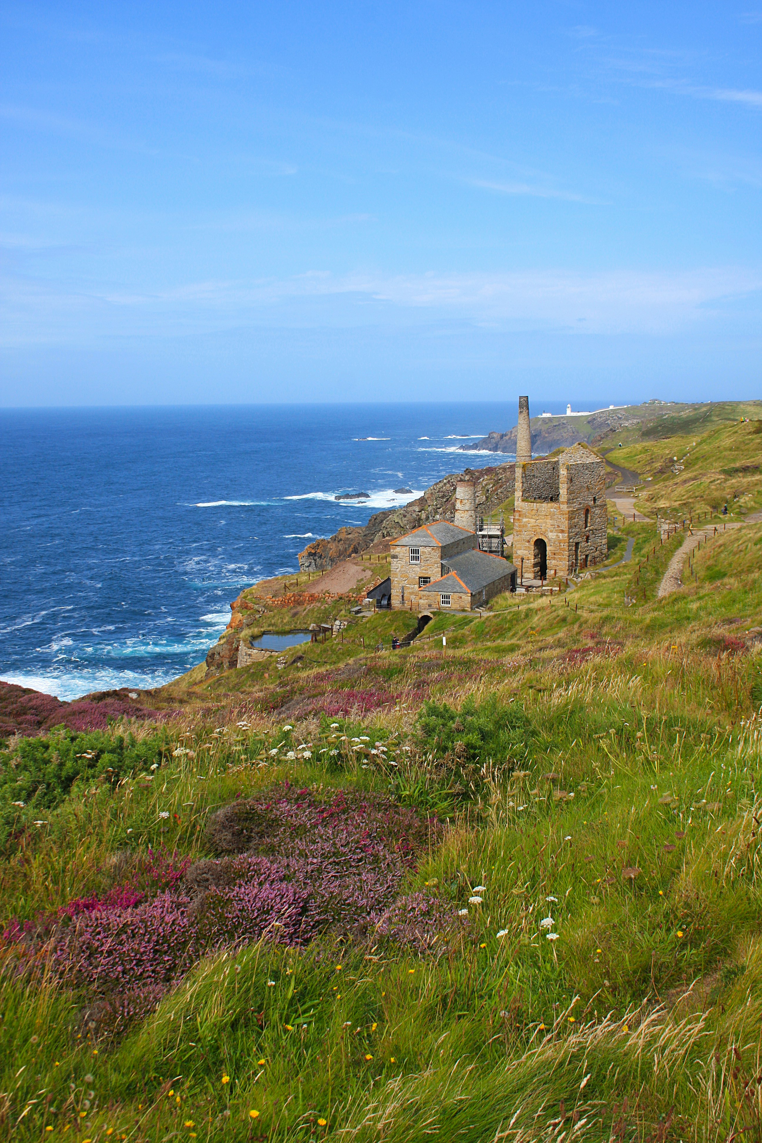 Historic mining ruins nestled in vibrant coastal vegetation, overlooking the ocean waves. The scene captures the serene blend of nature and heritage.