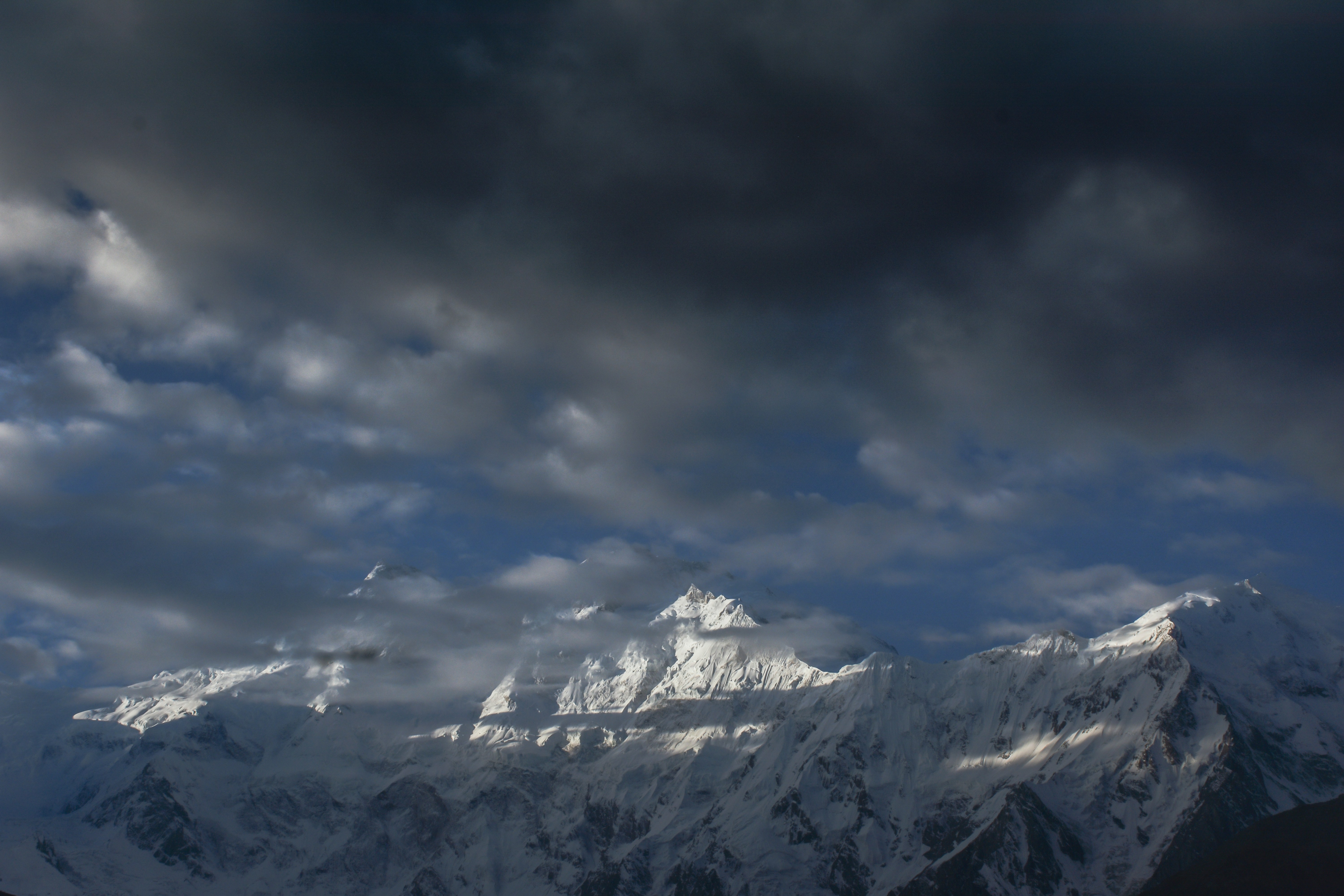 Snow-covered mountains illuminated under a dramatic, cloudy sky.