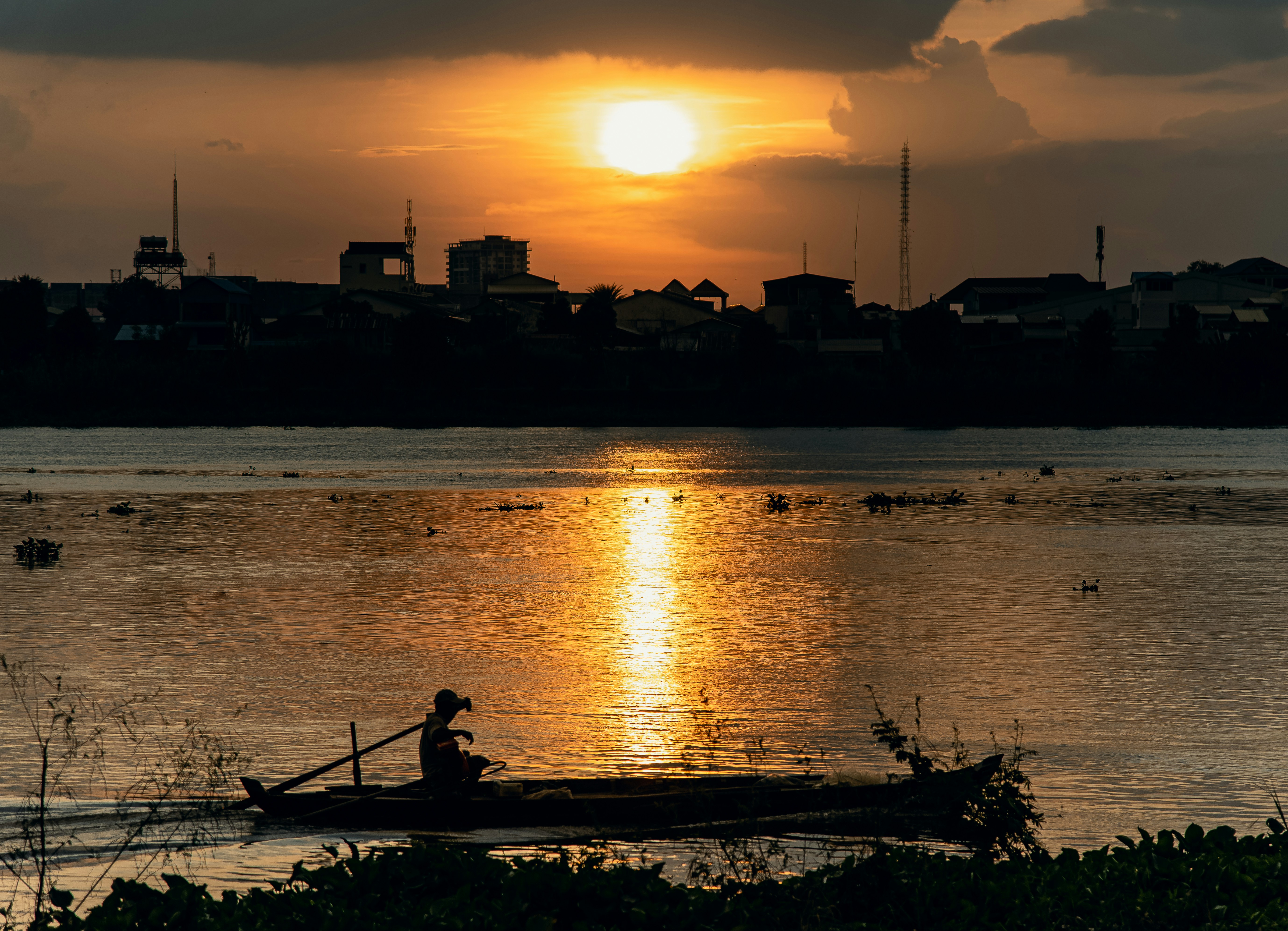 Silhouetted figure on a small boat gliding across a river during a golden sunset.