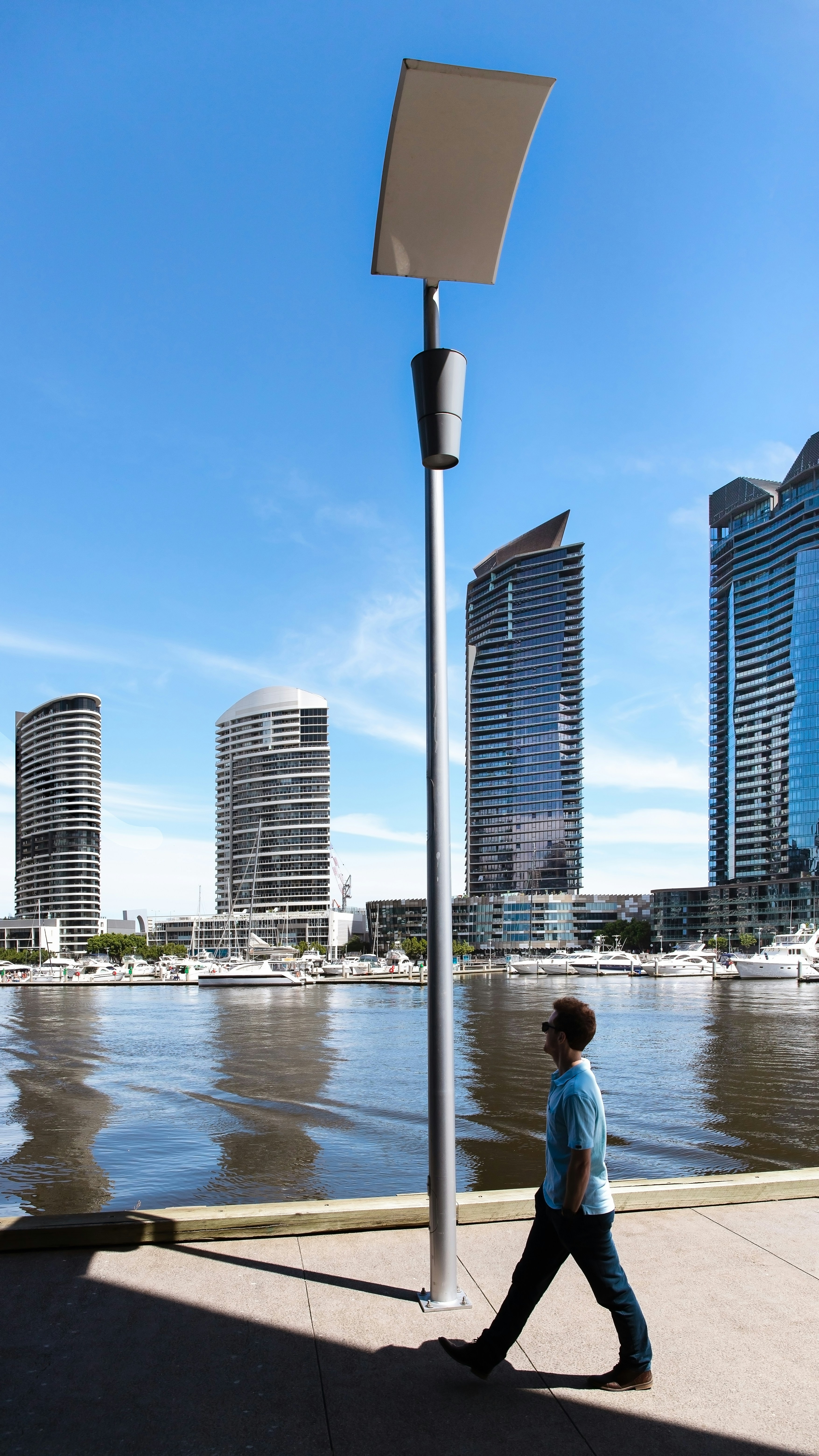 Sunlit Promenade: A Lone Pedestrian Beside a Modern Marina Tower