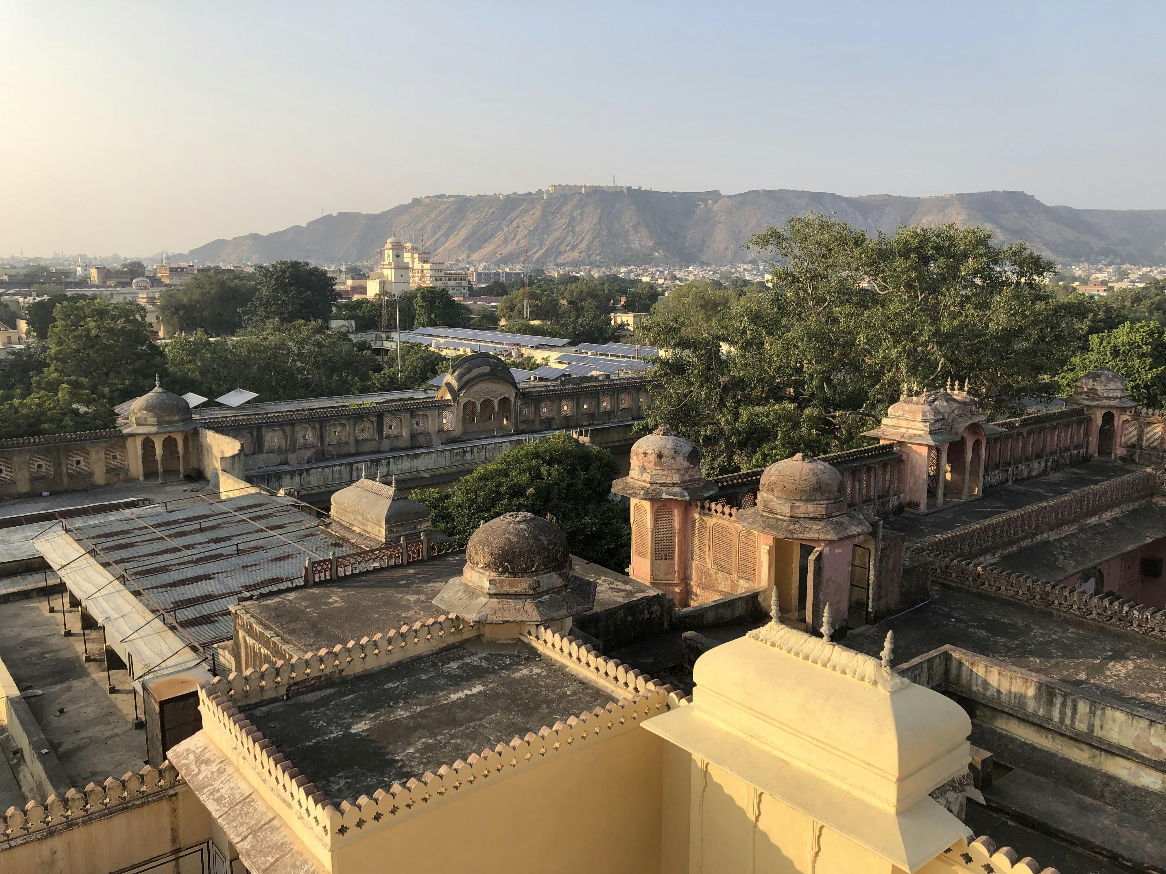 Panoramic view of Jaipur's historic architecture with lush greenery and distant hills. The scene captures the essence of the city's rich heritage.