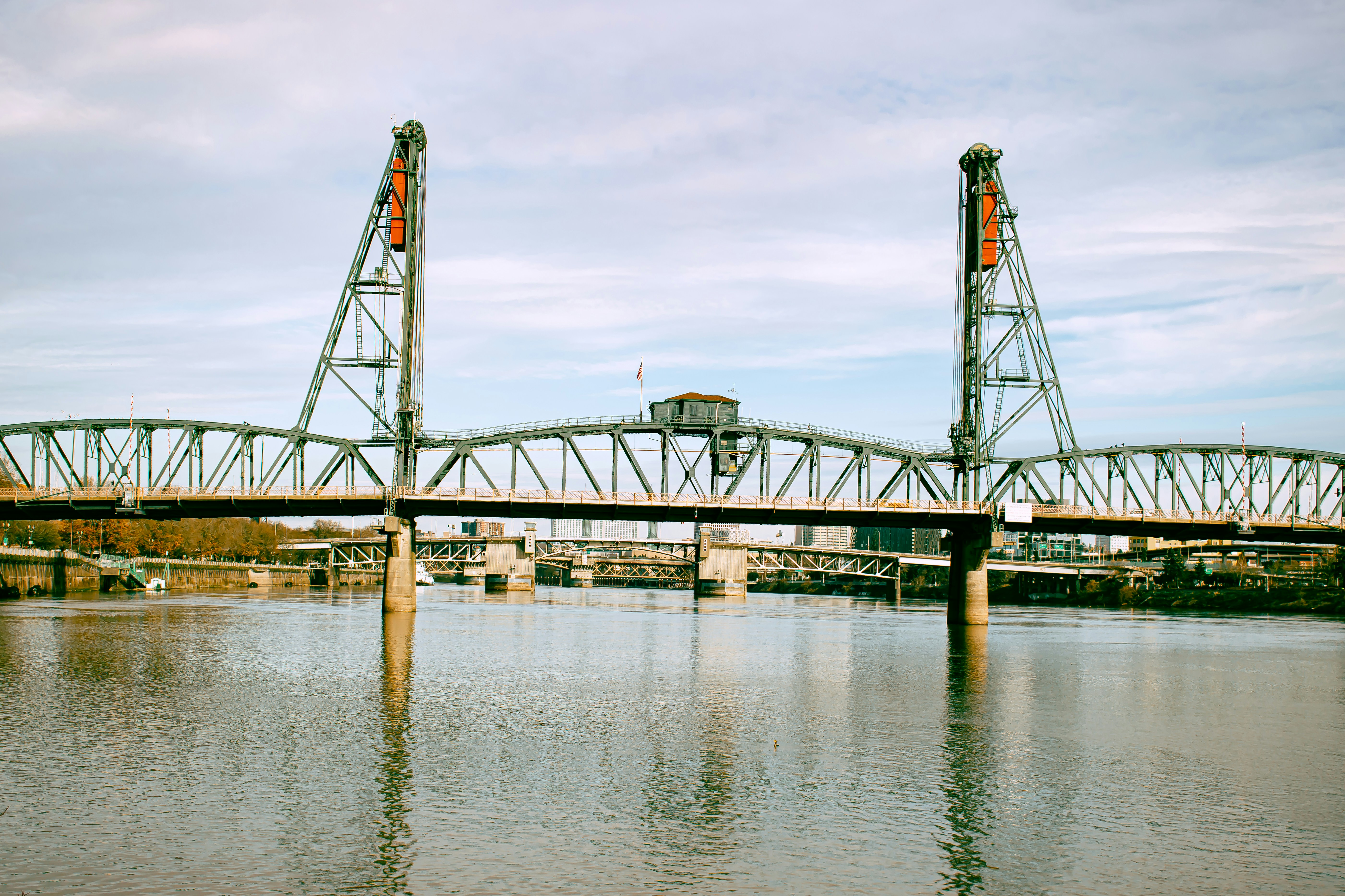Steel drawbridge spanning a calm river under a cloud-streaked sky.