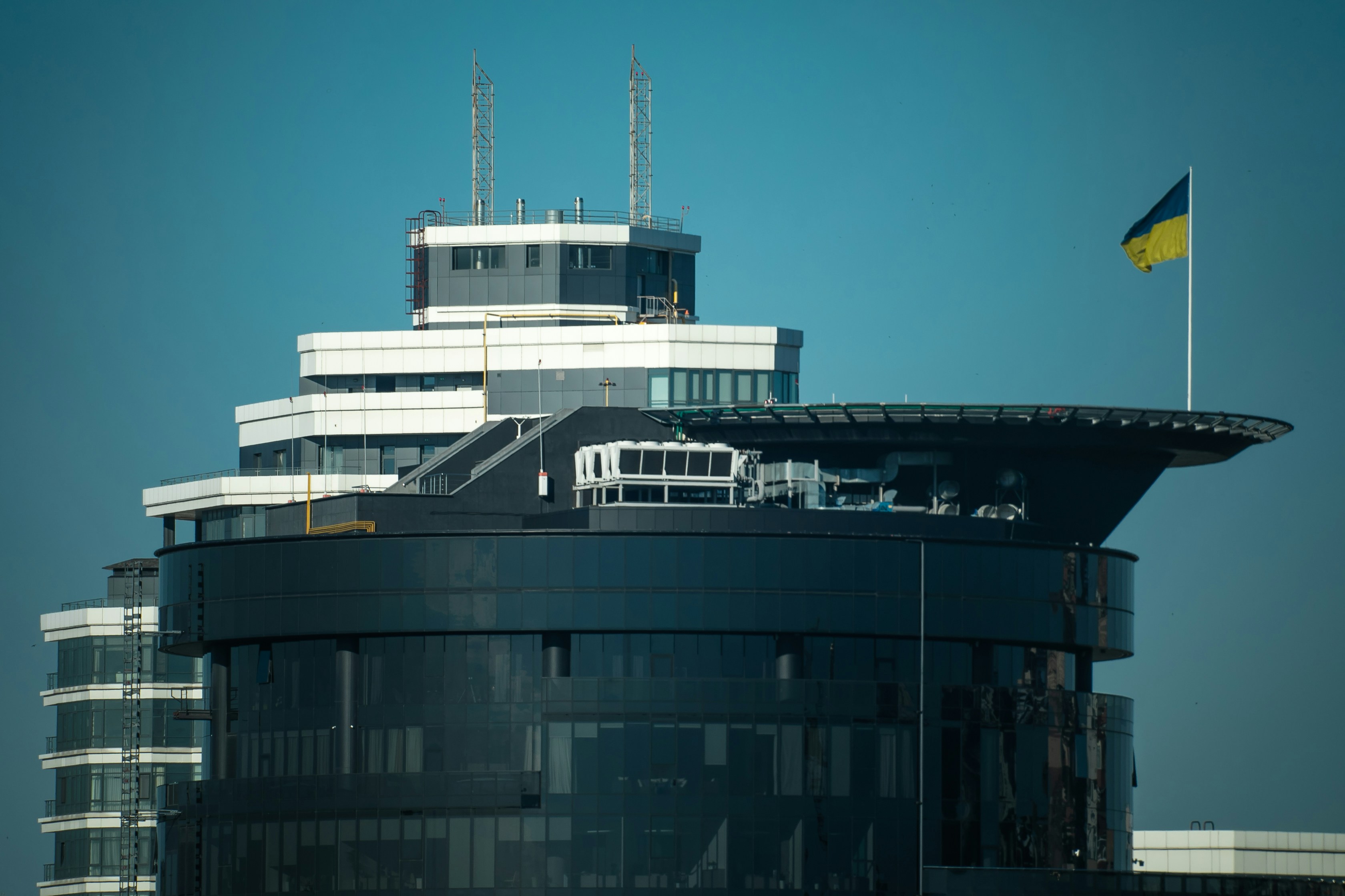 Contemporary skyscraper with a distinct rooftop design and a flag fluttering in the wind, showcasing urban architecture.
