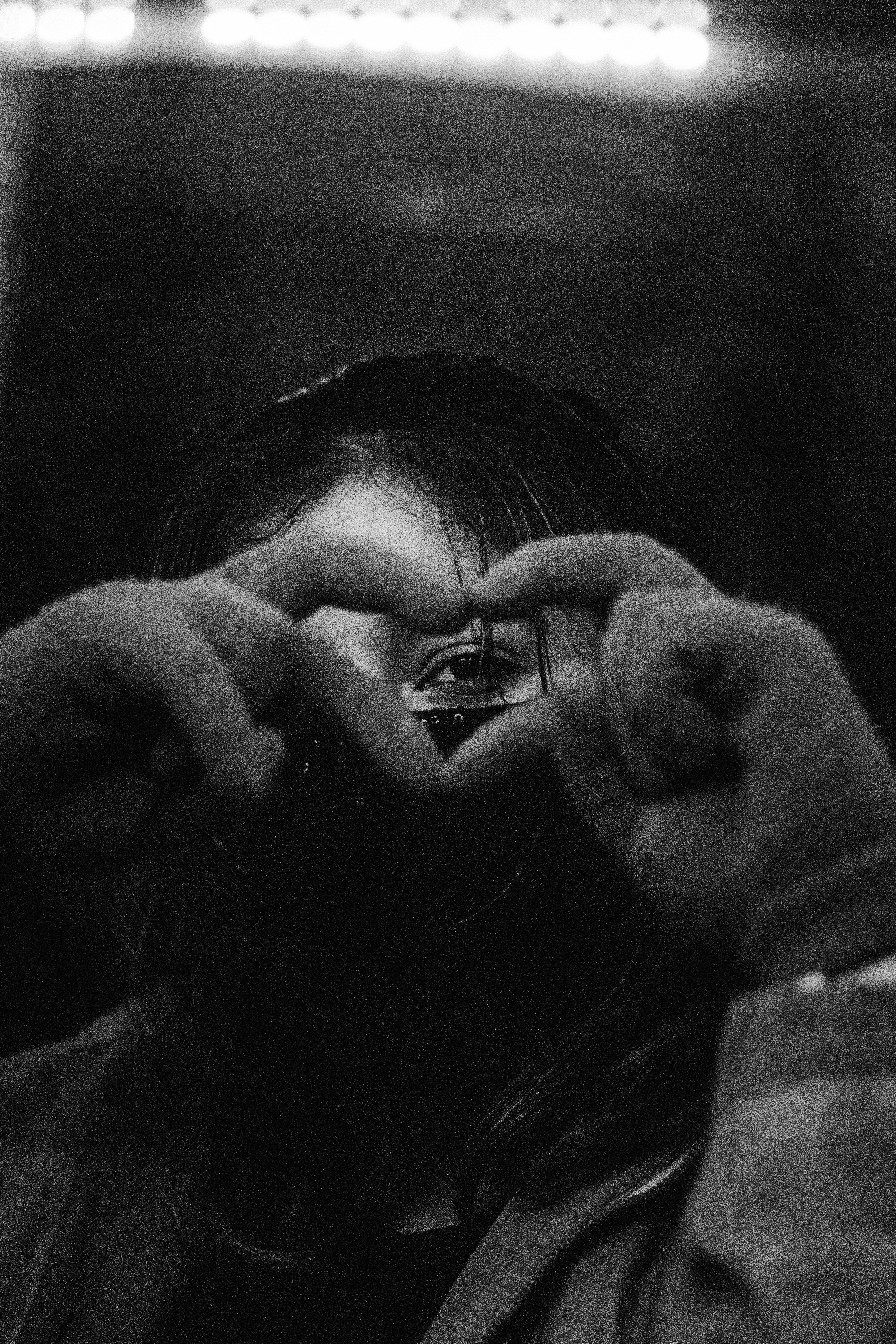 A person forms a heart shape with their hands, partially obscured by a mask, conveying a message of love amidst a dark backdrop.