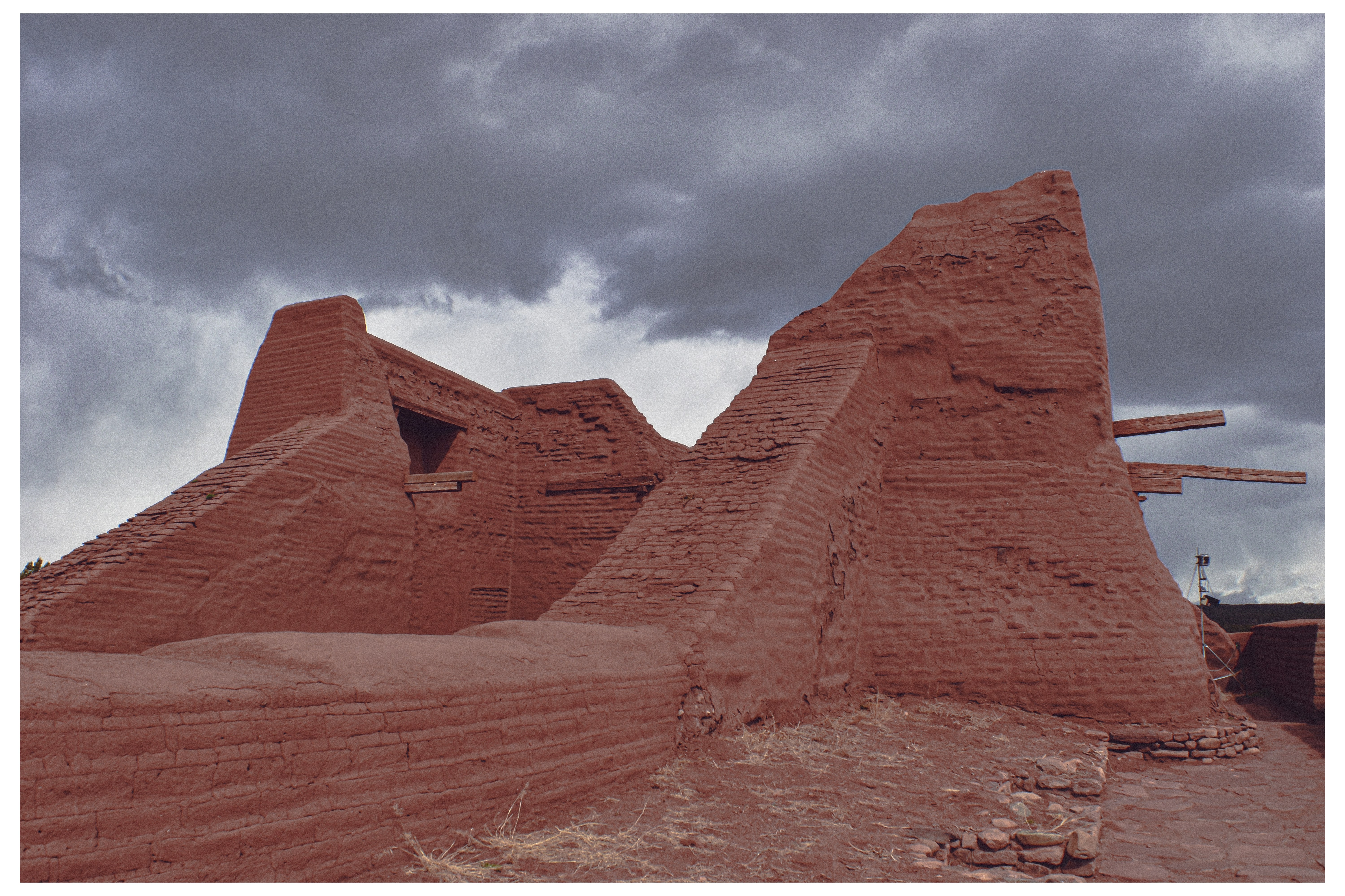 Weathered adobe structures rise against a moody sky, showcasing the artistry of ancient architecture. The interplay of light and shadow highlights the textural details of the clay walls.