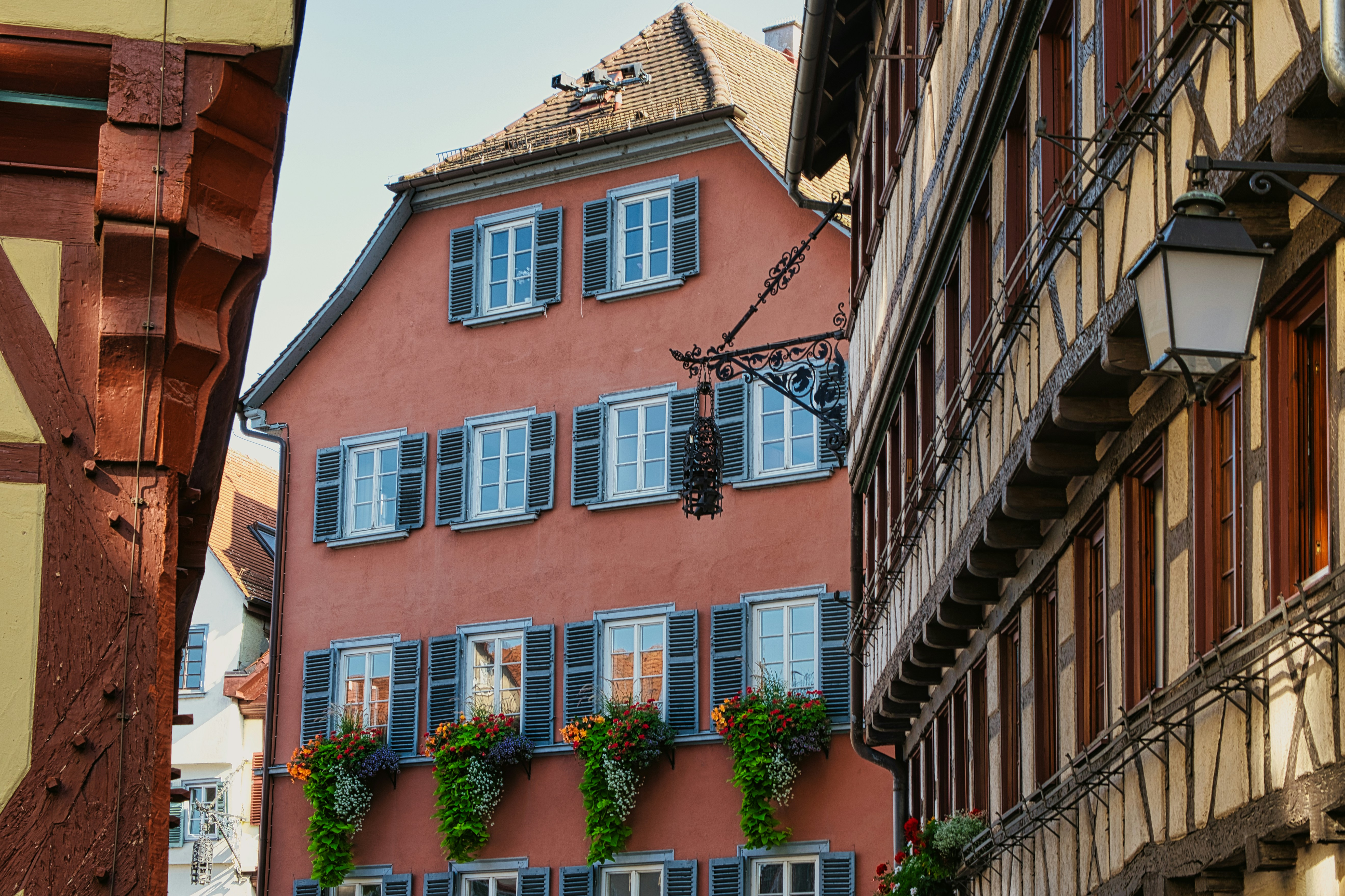 Red building with blue shutters and vibrant flower boxes framed by timber-framed structures under a clear sky.