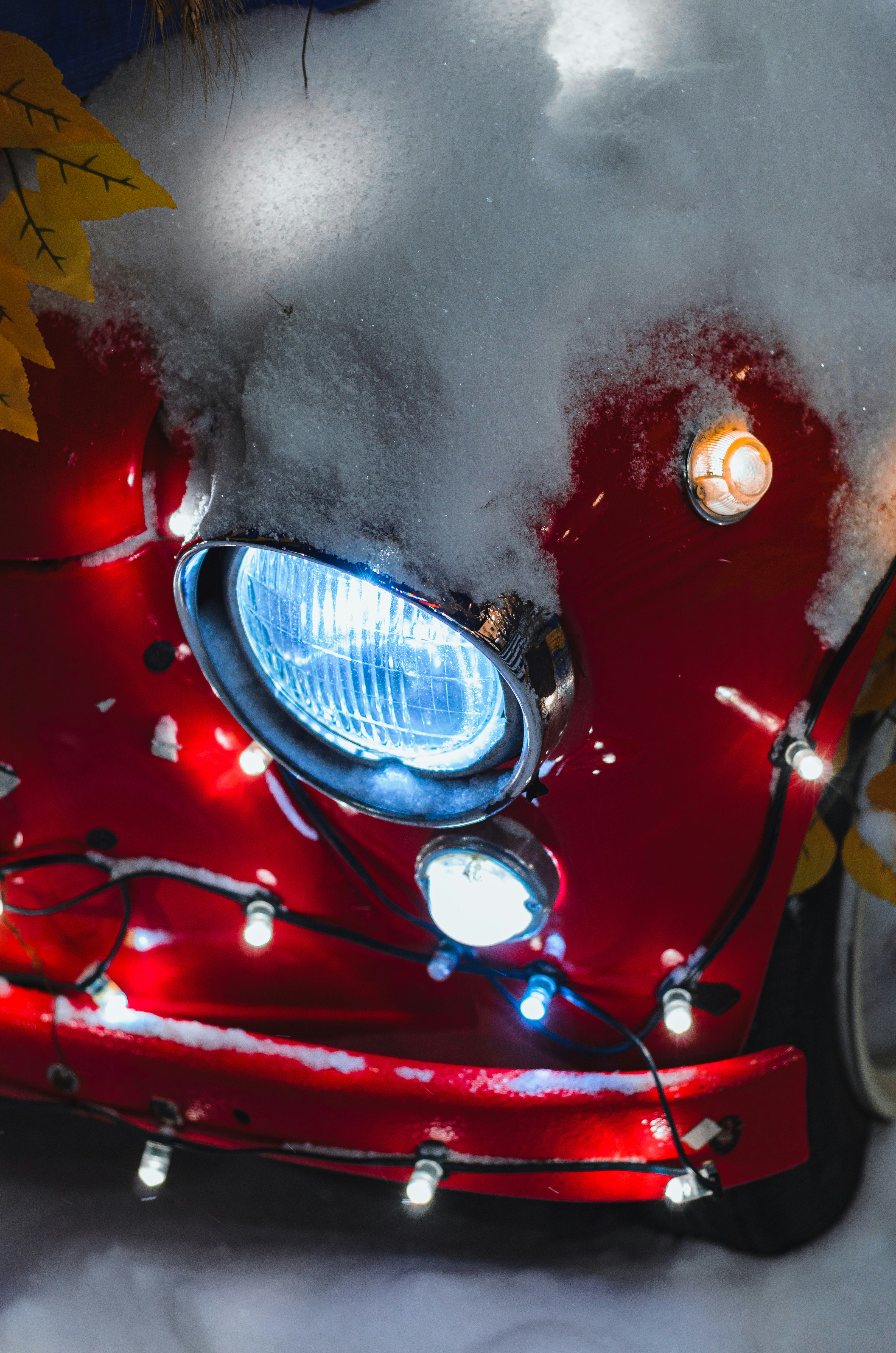 Snow-Wrapped Headlamp: A Red Vintage Car Draped in Holiday Lights