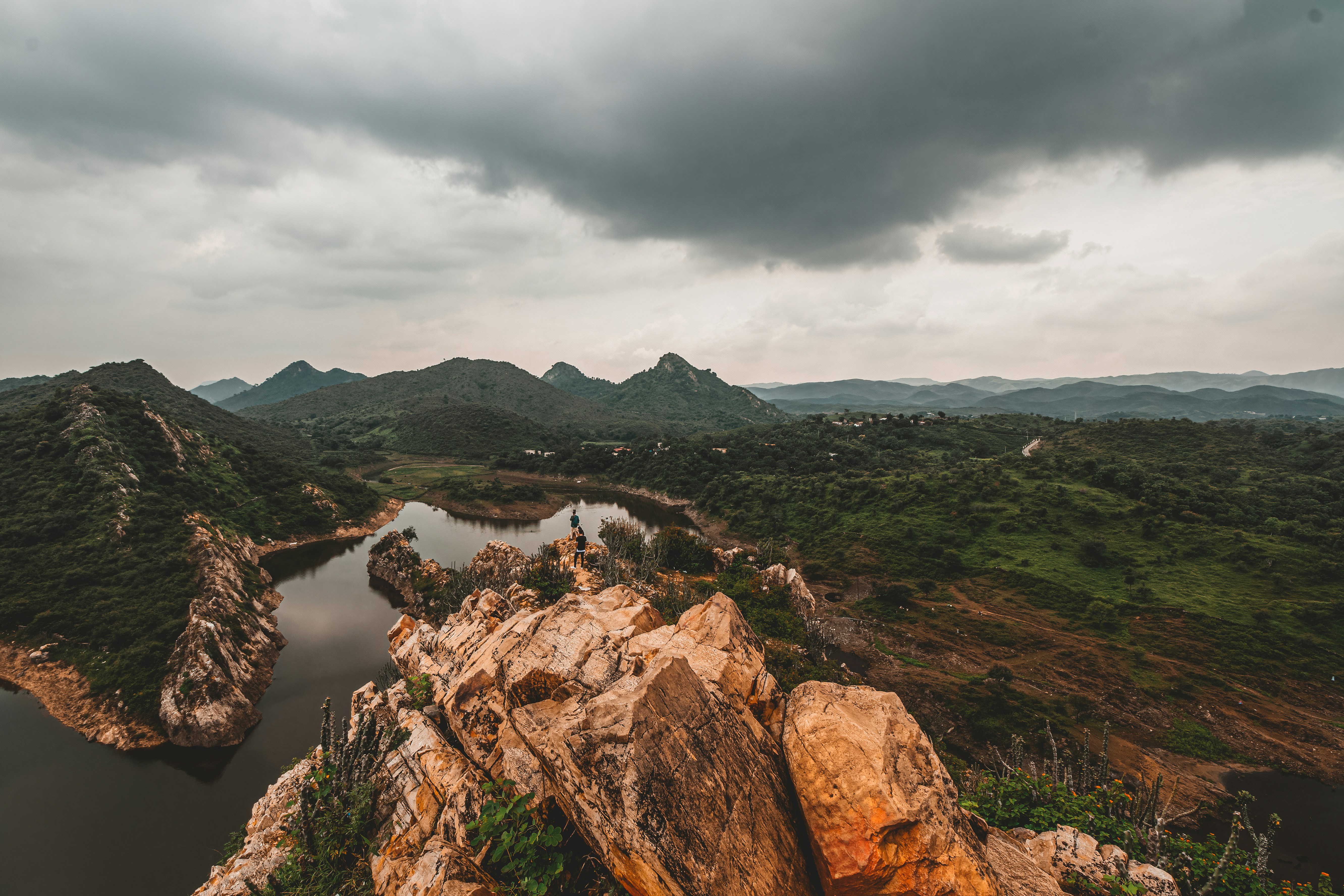 Dramatic clouds hover above a rocky landscape with a winding river and distant hills.