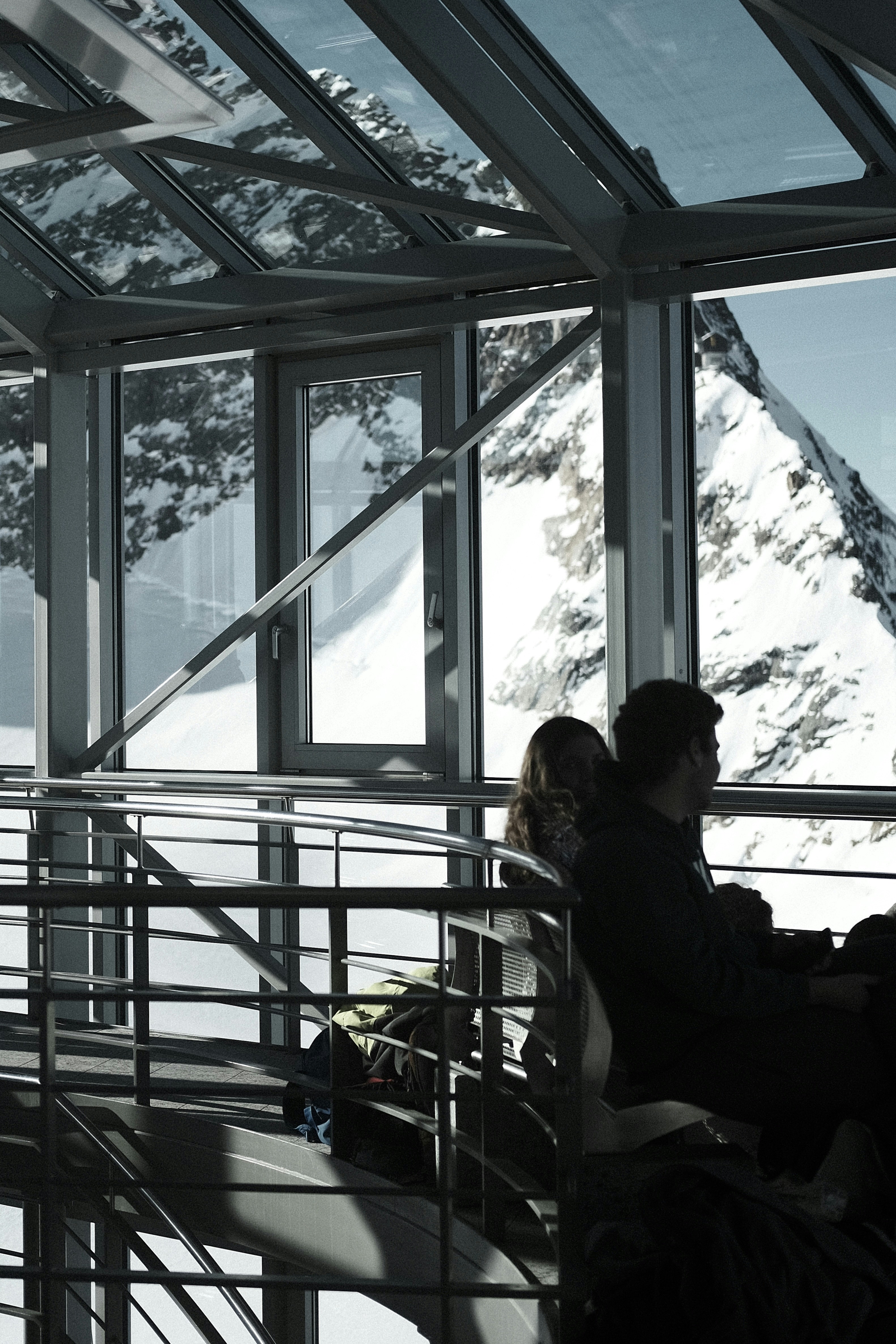 Alpine Atrium: Quiet Pause on a Glass Balcony Amid Snowy Peaks