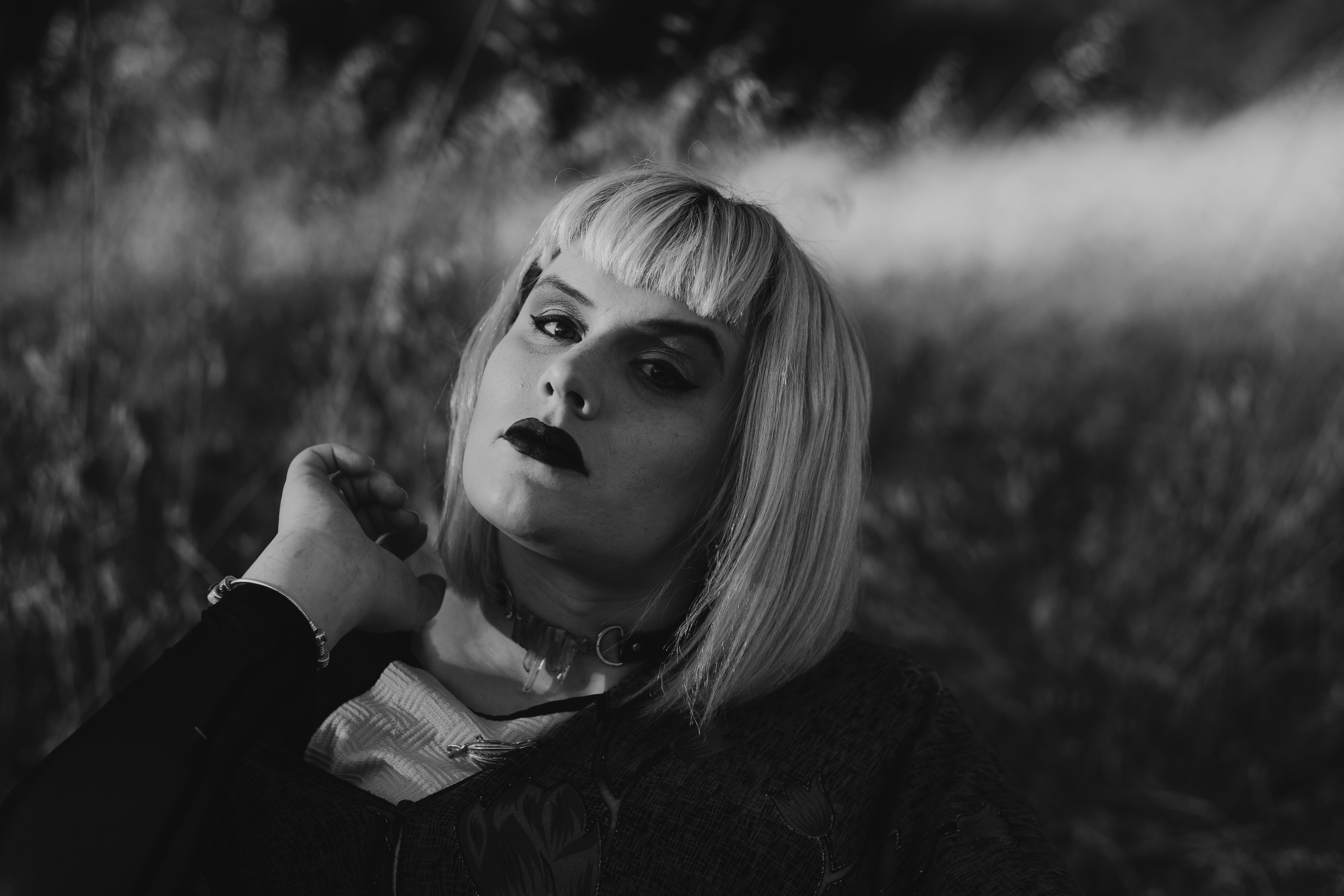 Person with short blonde hair and dark lipstick poses thoughtfully in a sunlit field.