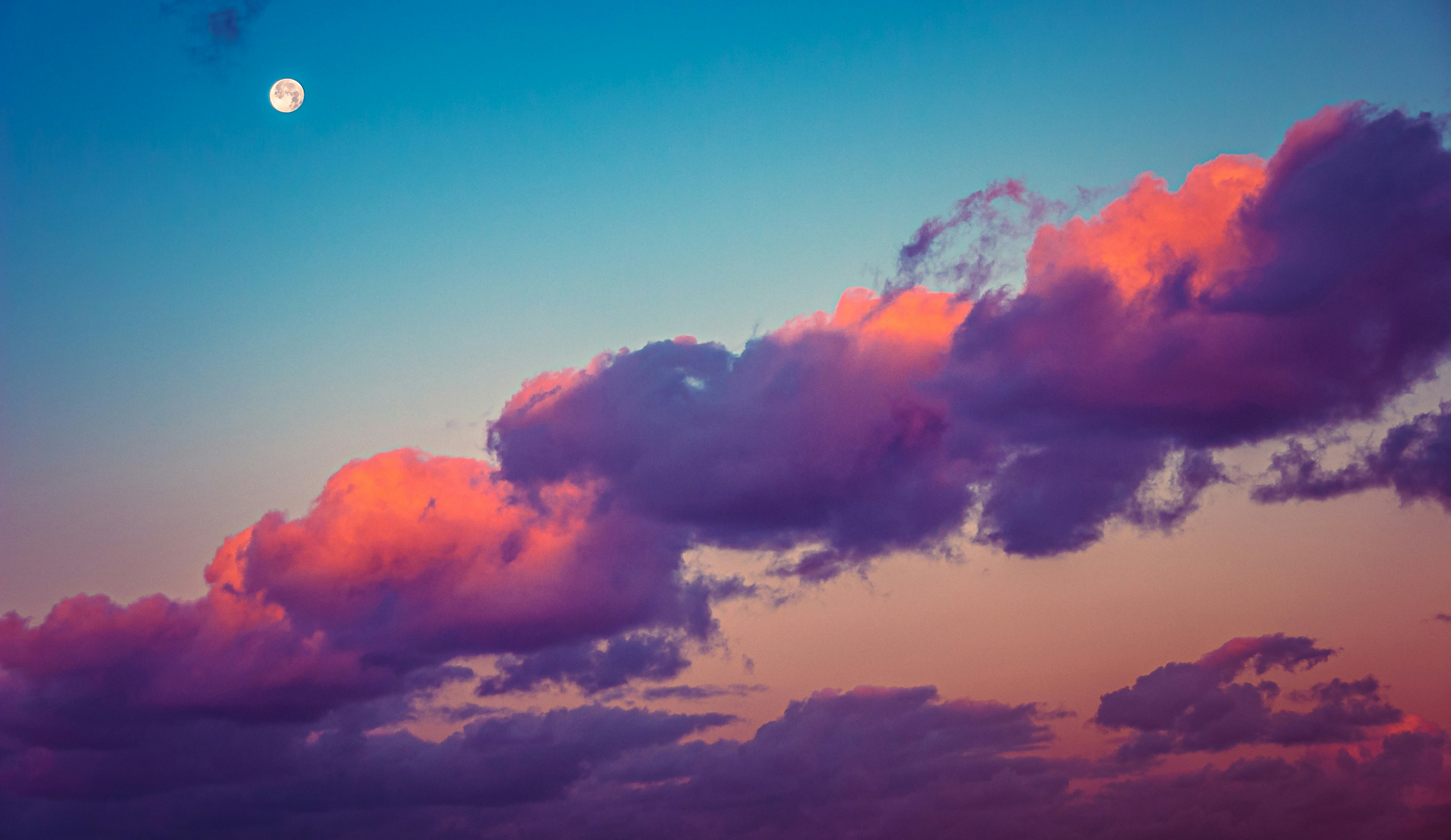 Airplane traversing a vibrant twilight sky with a prominent moon and colorful clouds.