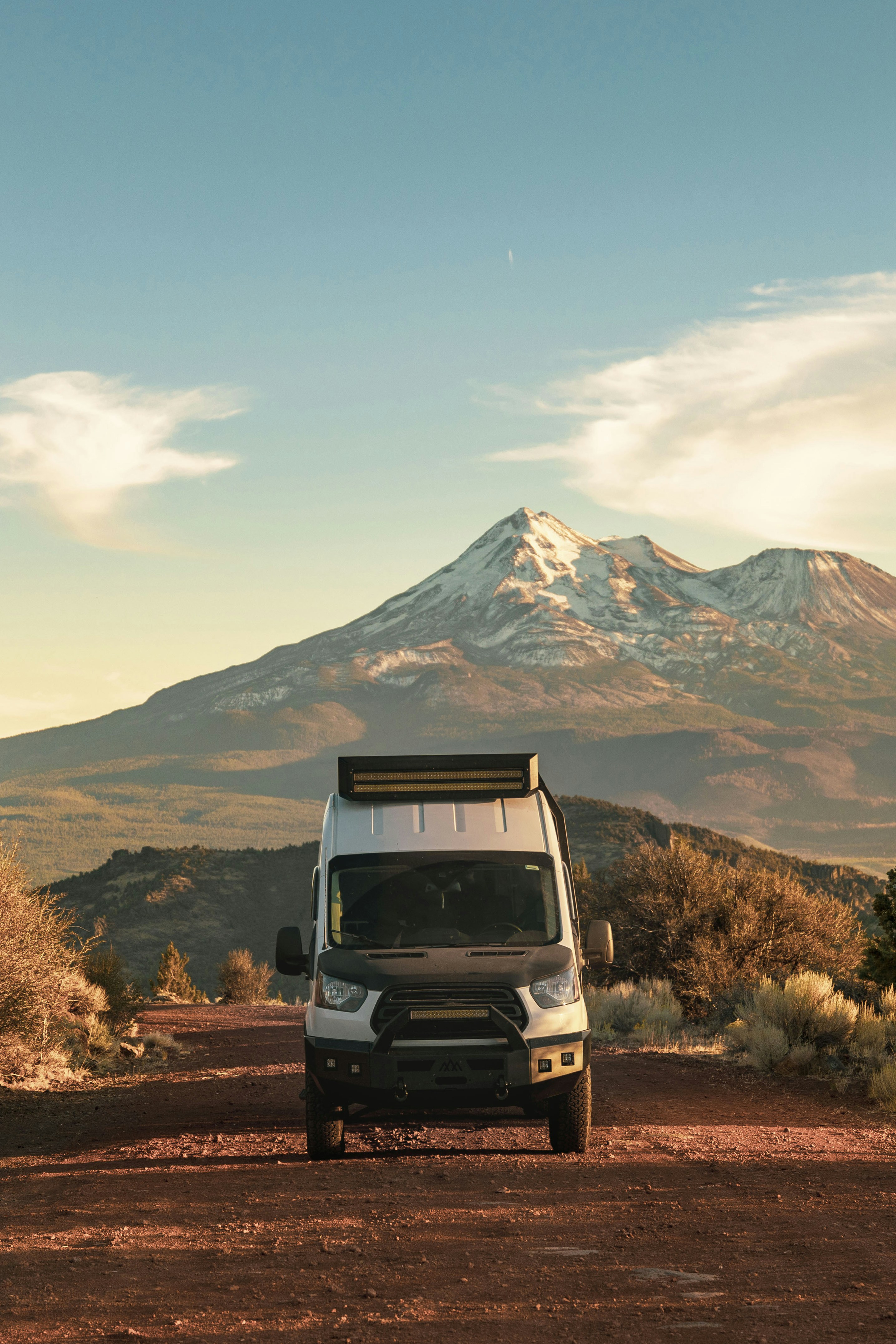 A rugged camper van parked on a dirt road with a stunning mountain backdrop, showcasing the beauty of nature. The scene captures the spirit of adventure and exploration.