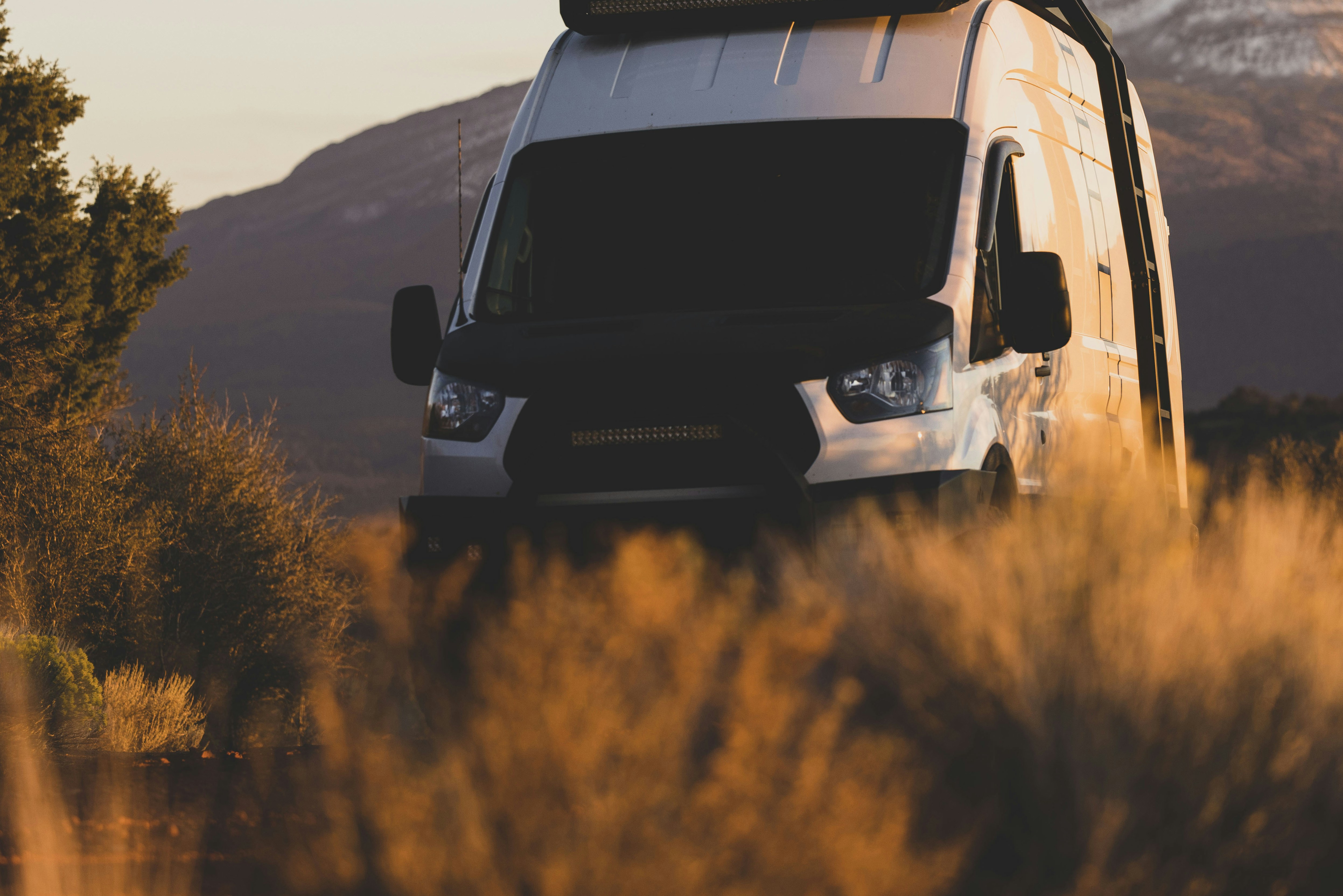 A white van parked amidst golden grasses and distant mountains, capturing the essence of adventure in nature's embrace.