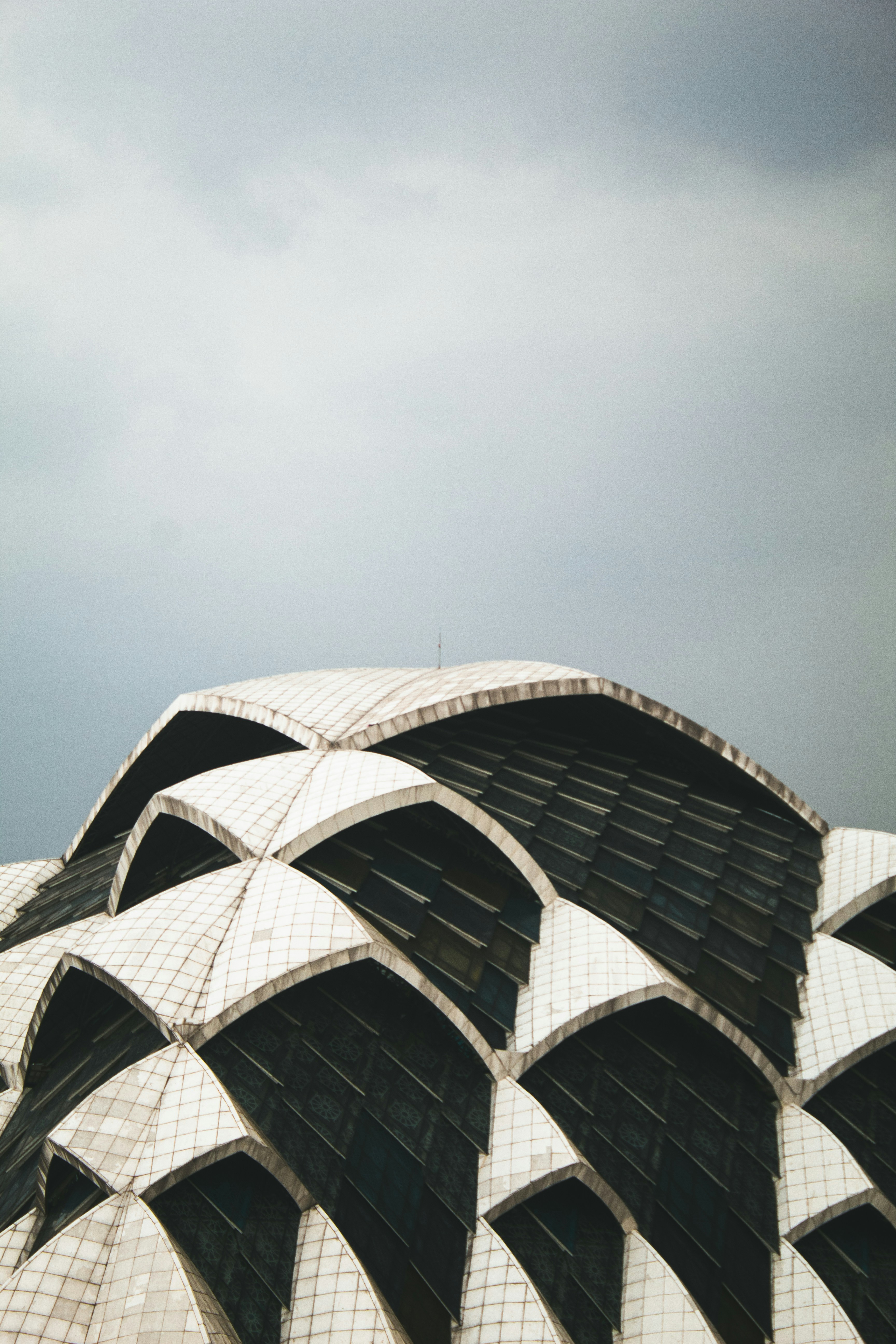 Intricate rooftop design of a modern building, showcasing geometric patterns and contrasting textures against a cloudy backdrop.