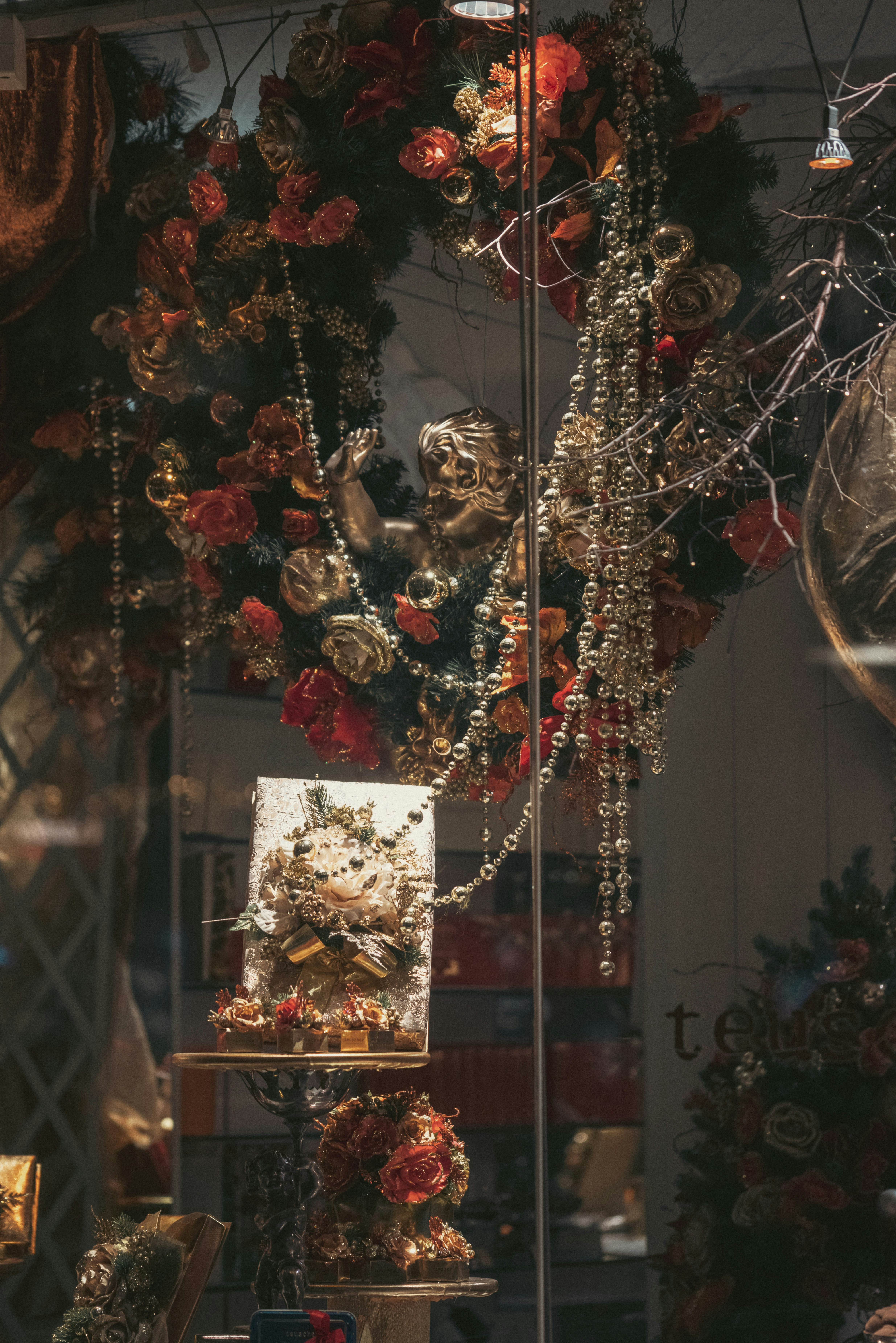 A beautifully arranged holiday display featuring a golden wreath adorned with roses and sparkling beads, alongside a decorative gift box. The scene captures the essence of festive cheer.