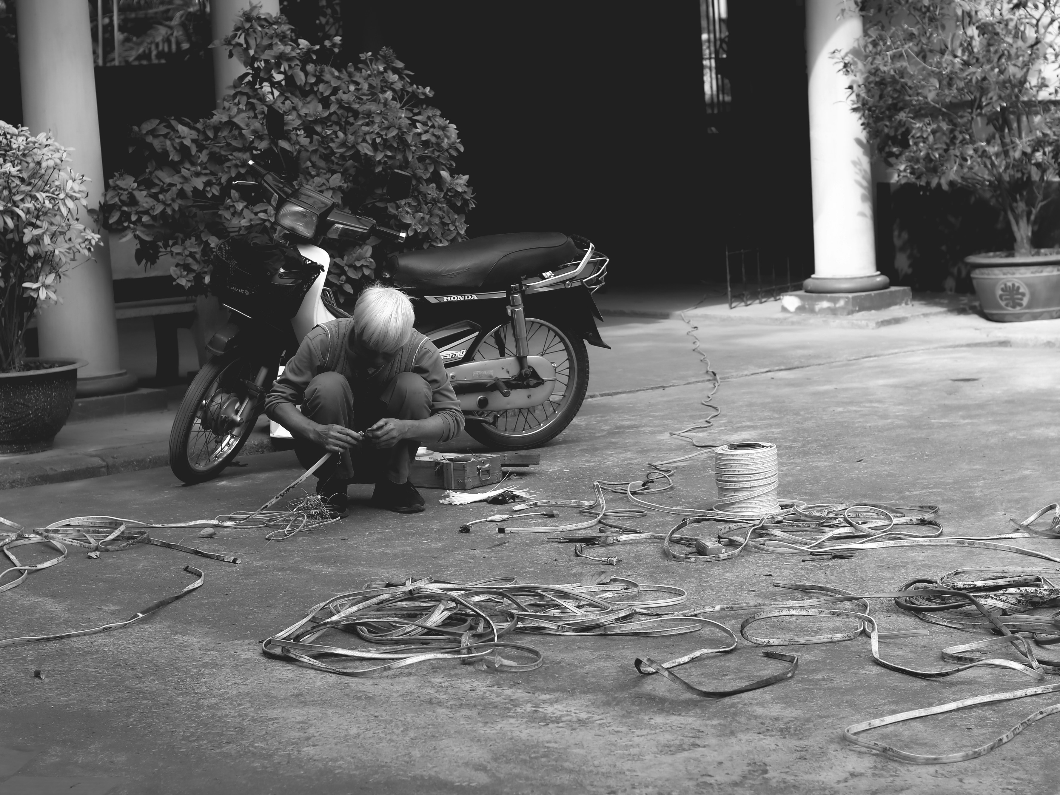 A craftsman meticulously working with wires on a concrete surface, surrounded by an array of tangled materials. The scene captures the essence of dedication and craftsmanship.