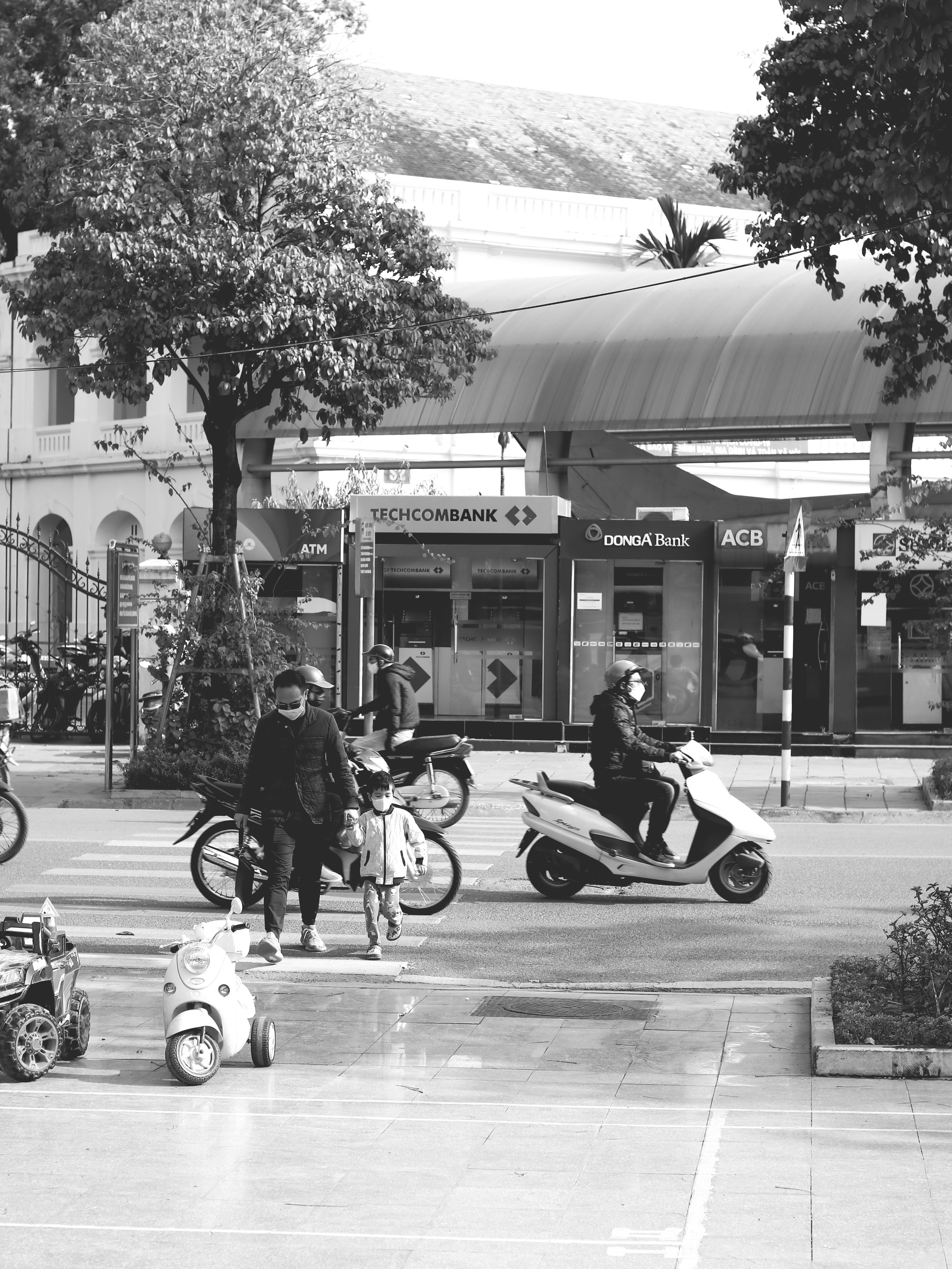 Monochrome Crosswalk: Families and Scooters in Front of a Bank Row