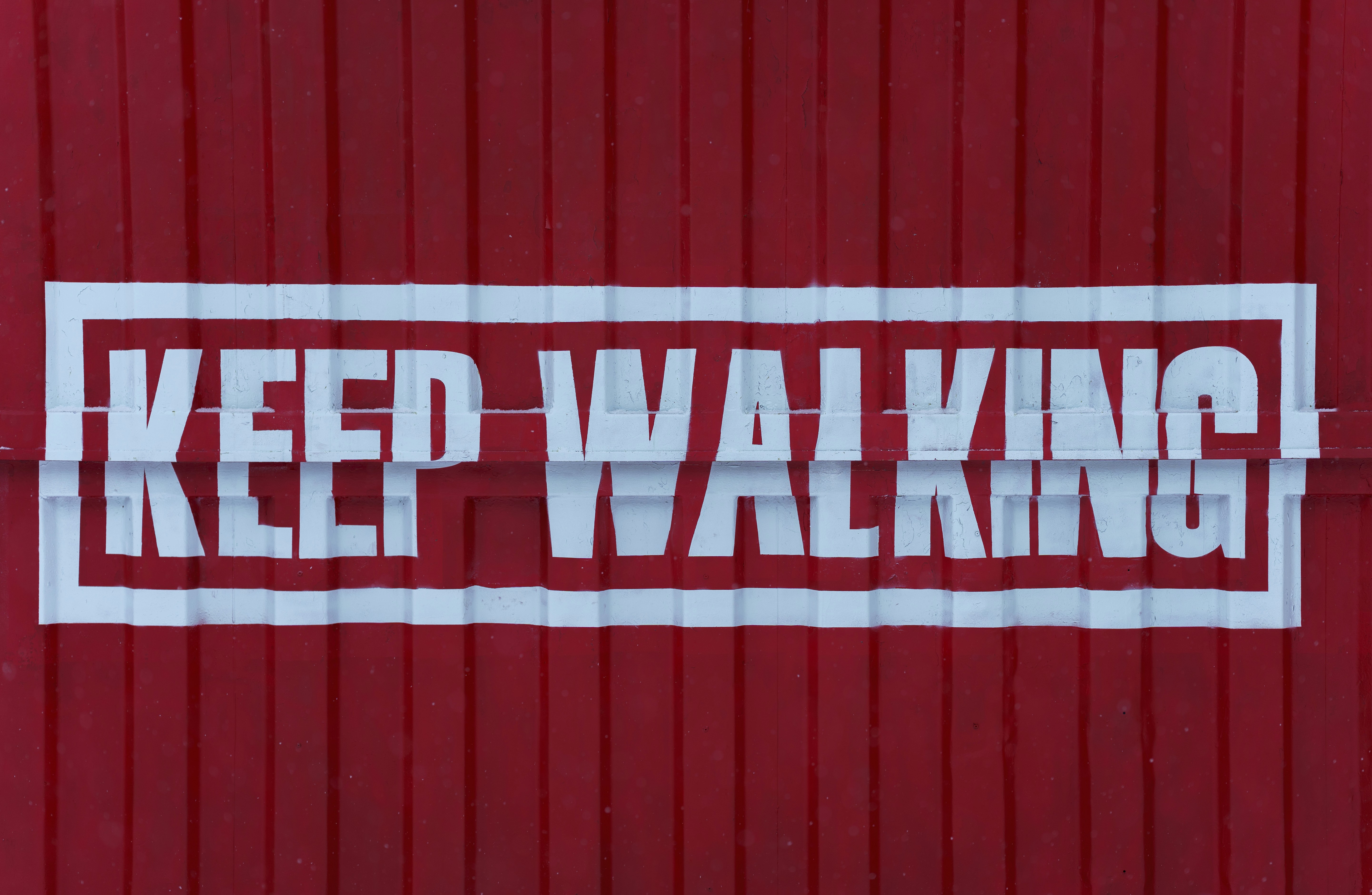 A red wall with a white keep walking sticker on it photo – Free Logo ...