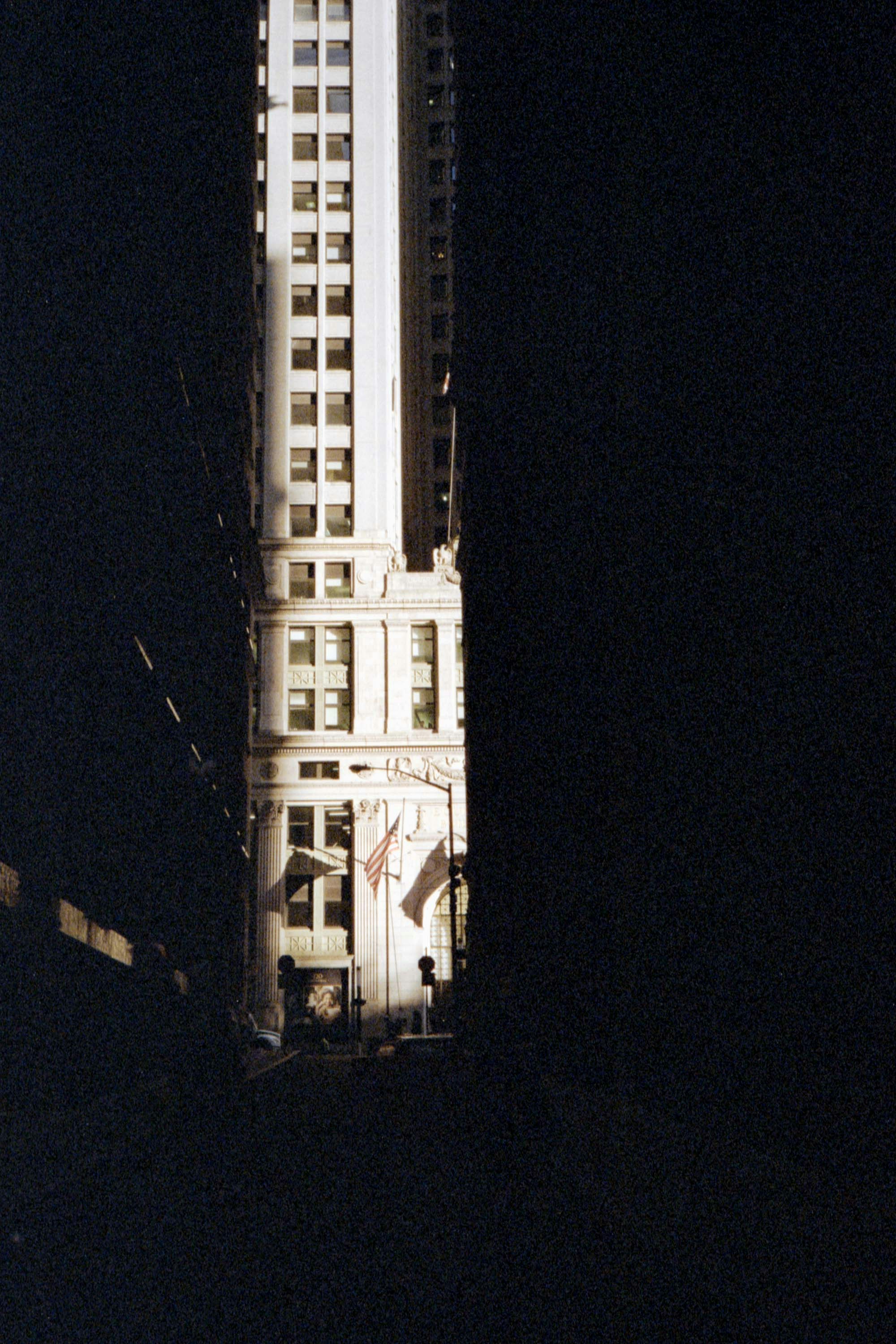 Illuminated building facade peeking through a narrow urban canyon at dusk, showcasing architectural details against a dark backdrop.