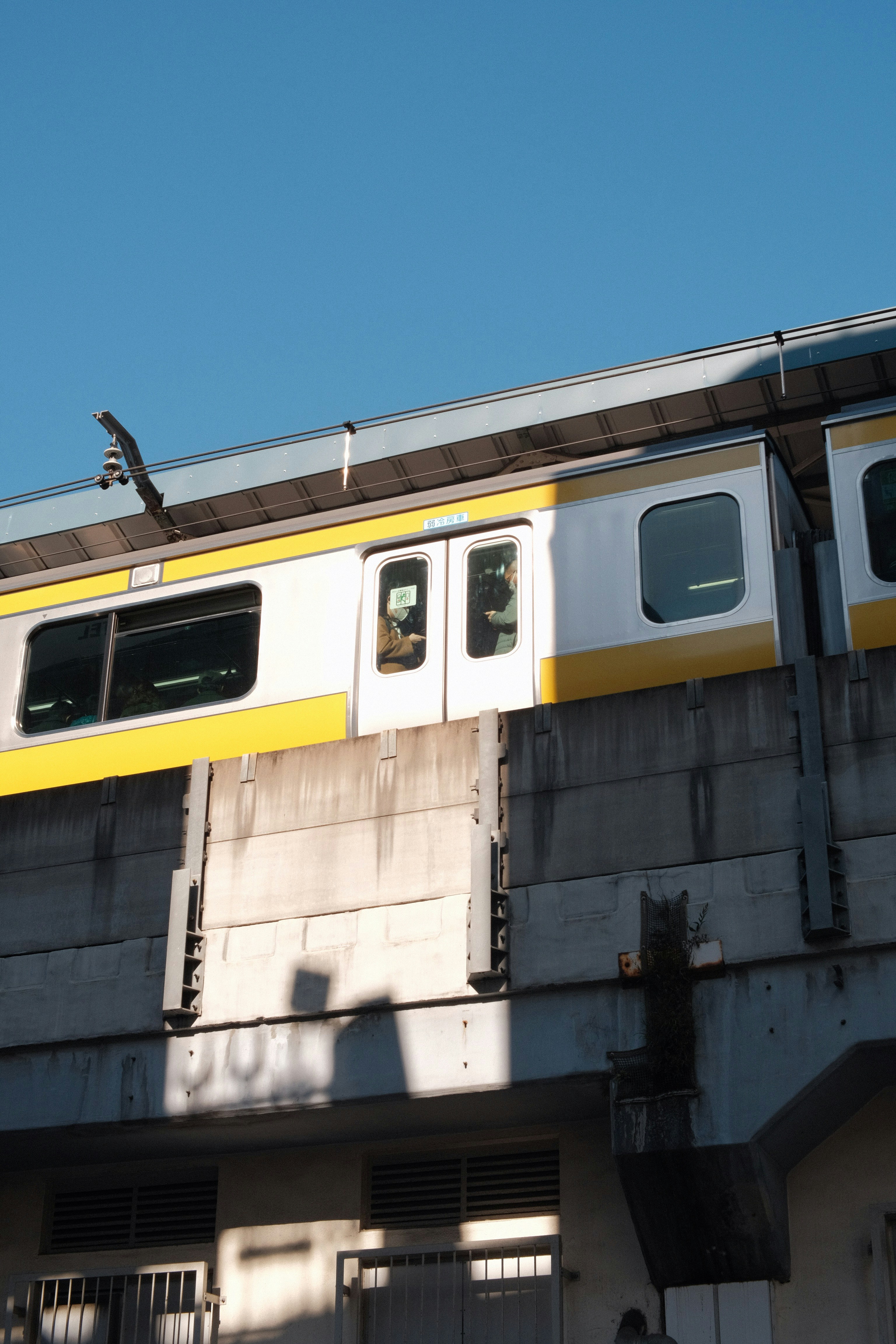 a yellow and white train traveling past a tall building