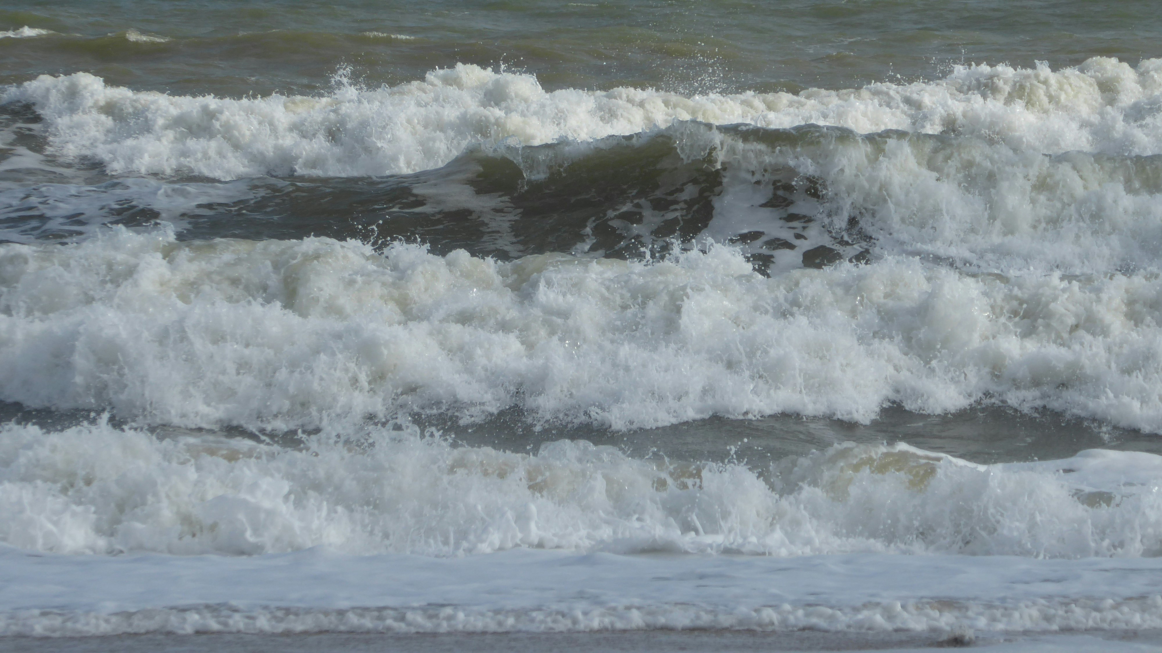 Rolling ocean waves crash with frothy white crests under a cloudy sky.