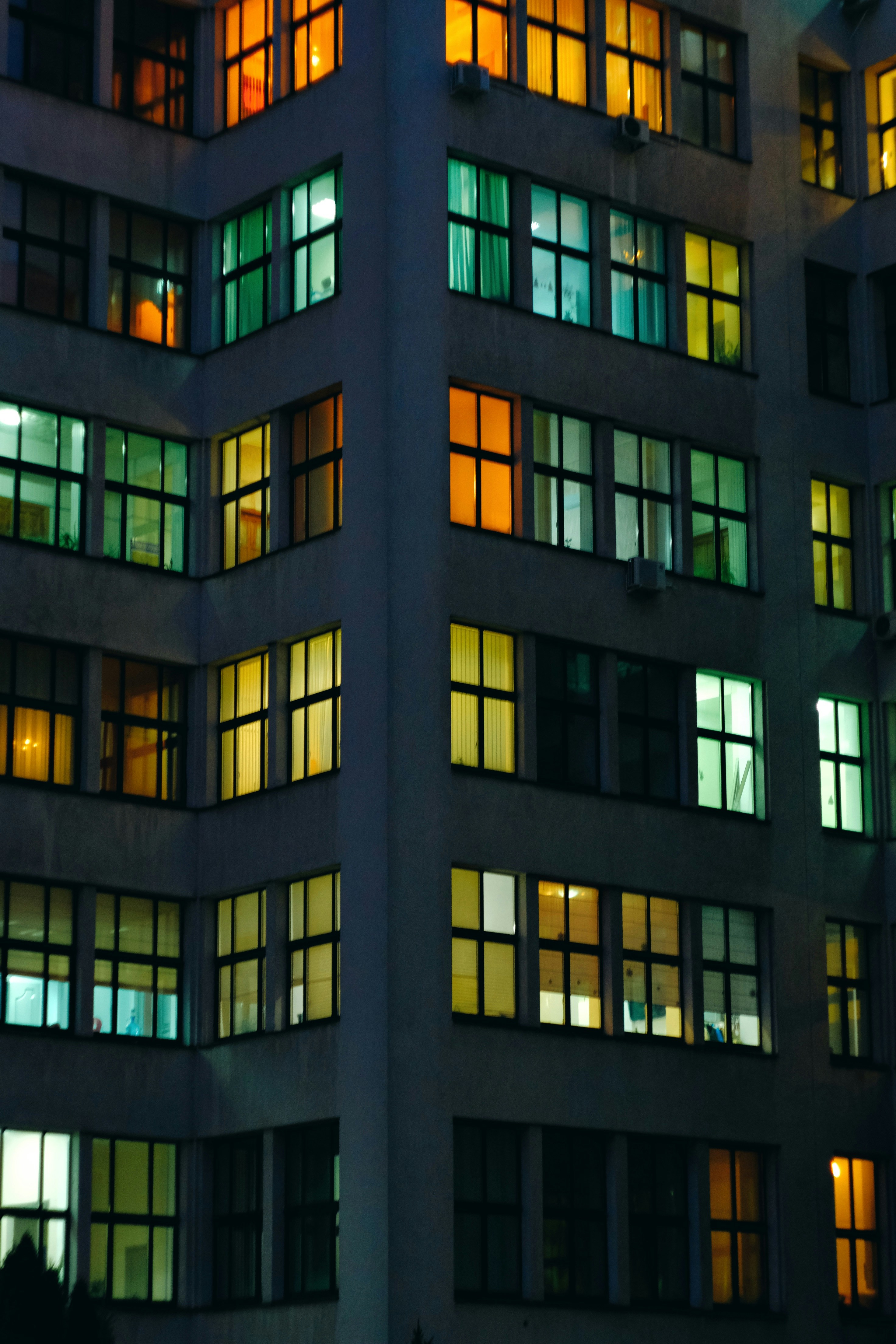 Illuminated windows of a modern building at night, showcasing a vibrant array of colors and reflections. The scene captures the essence of urban living.