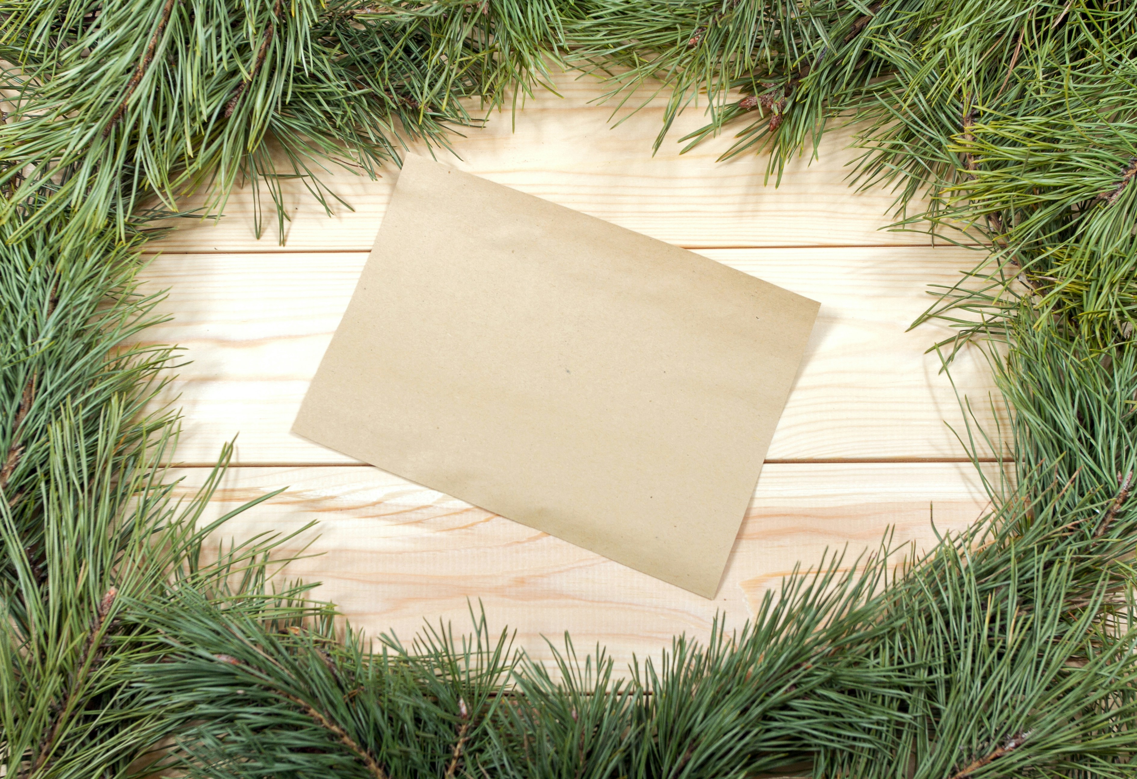 Brown envelope nestled within a lush pine wreath on a wooden surface, evoking a festive atmosphere.