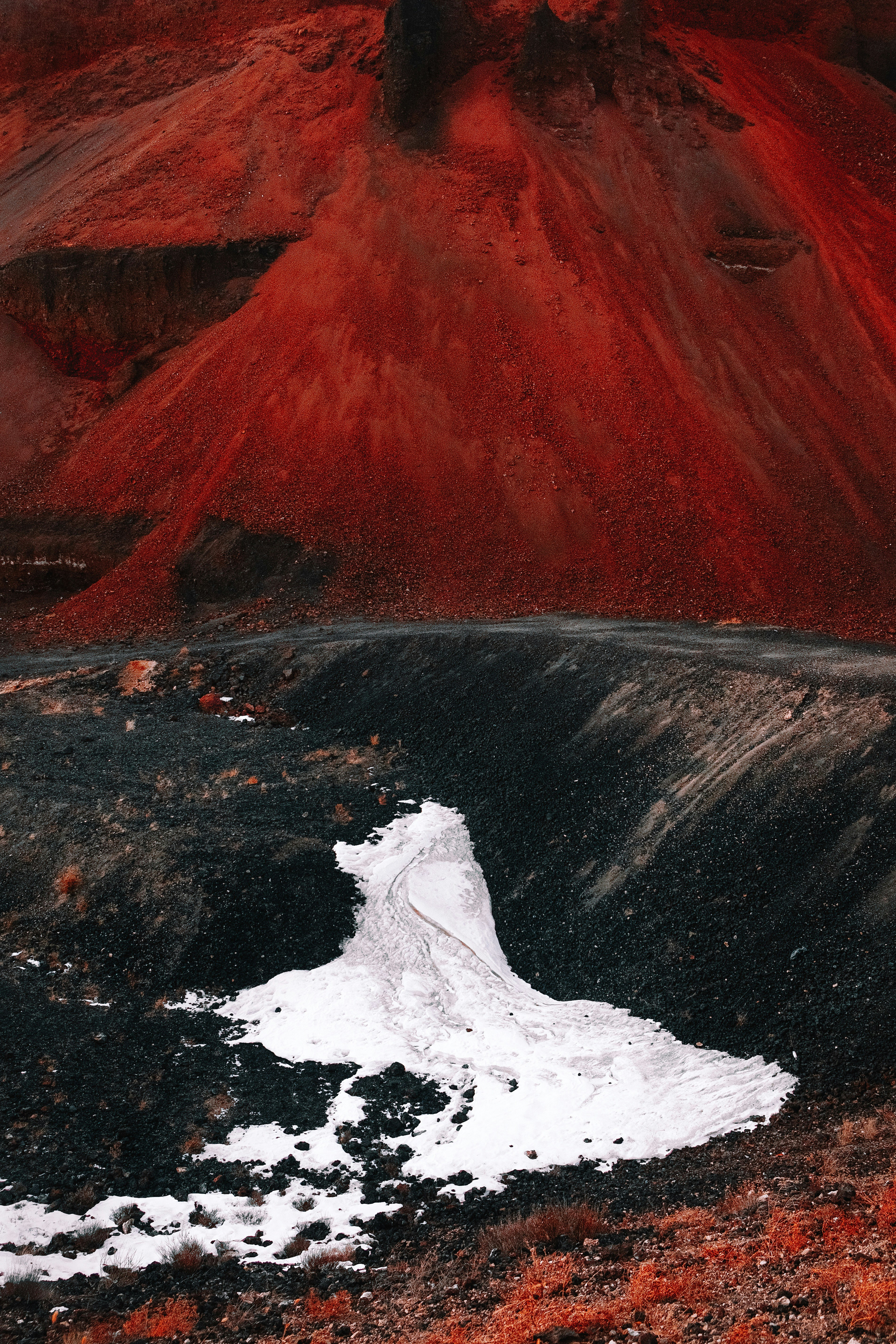 Contrast of vibrant red volcanic terrain with a patch of melting snow, showcasing nature's dramatic interplay. The scene captures the raw beauty of a volcanic landscape.
