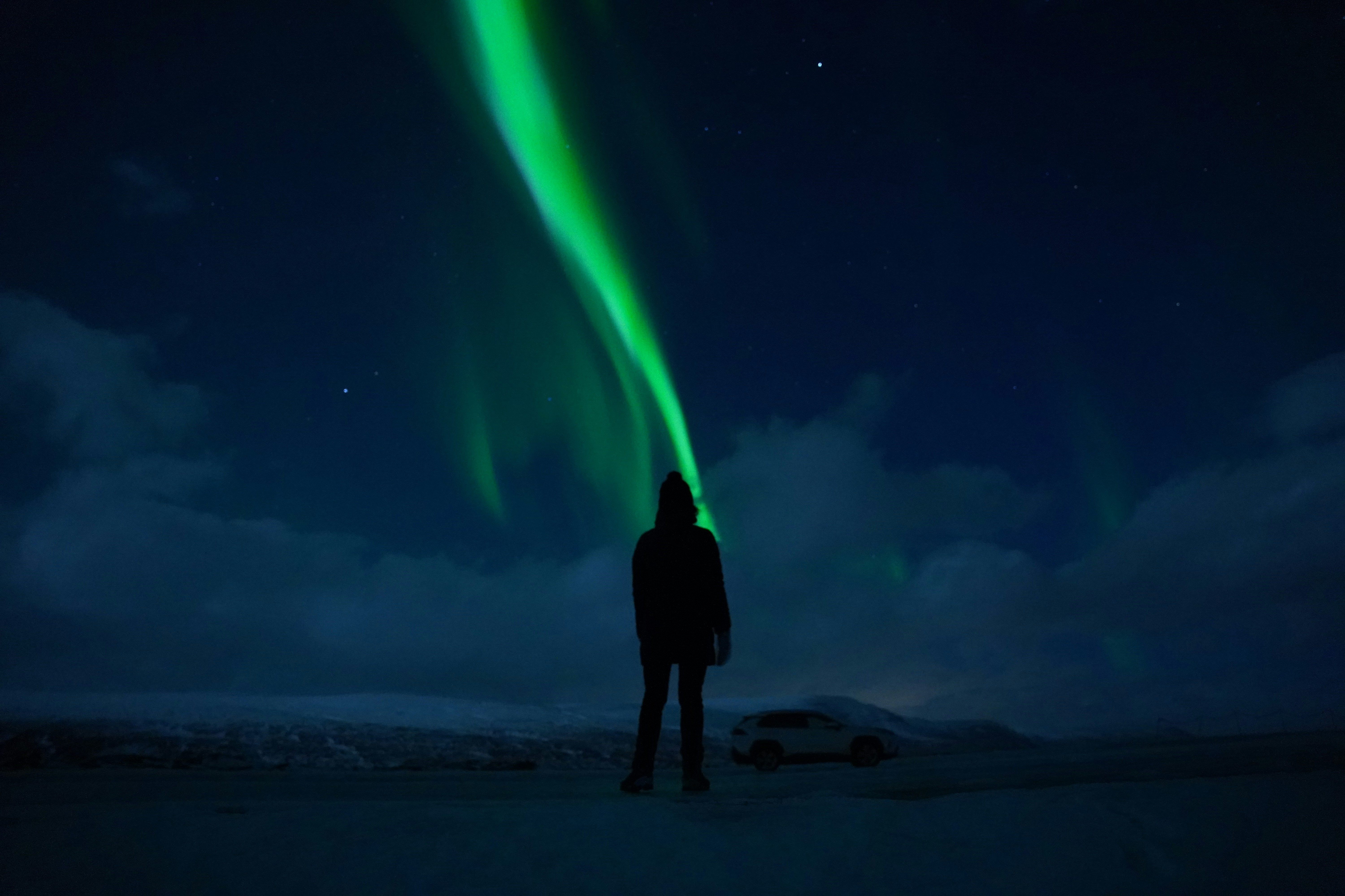 Silhouette of a figure standing against a backdrop of the vibrant northern lights illuminating the night sky.