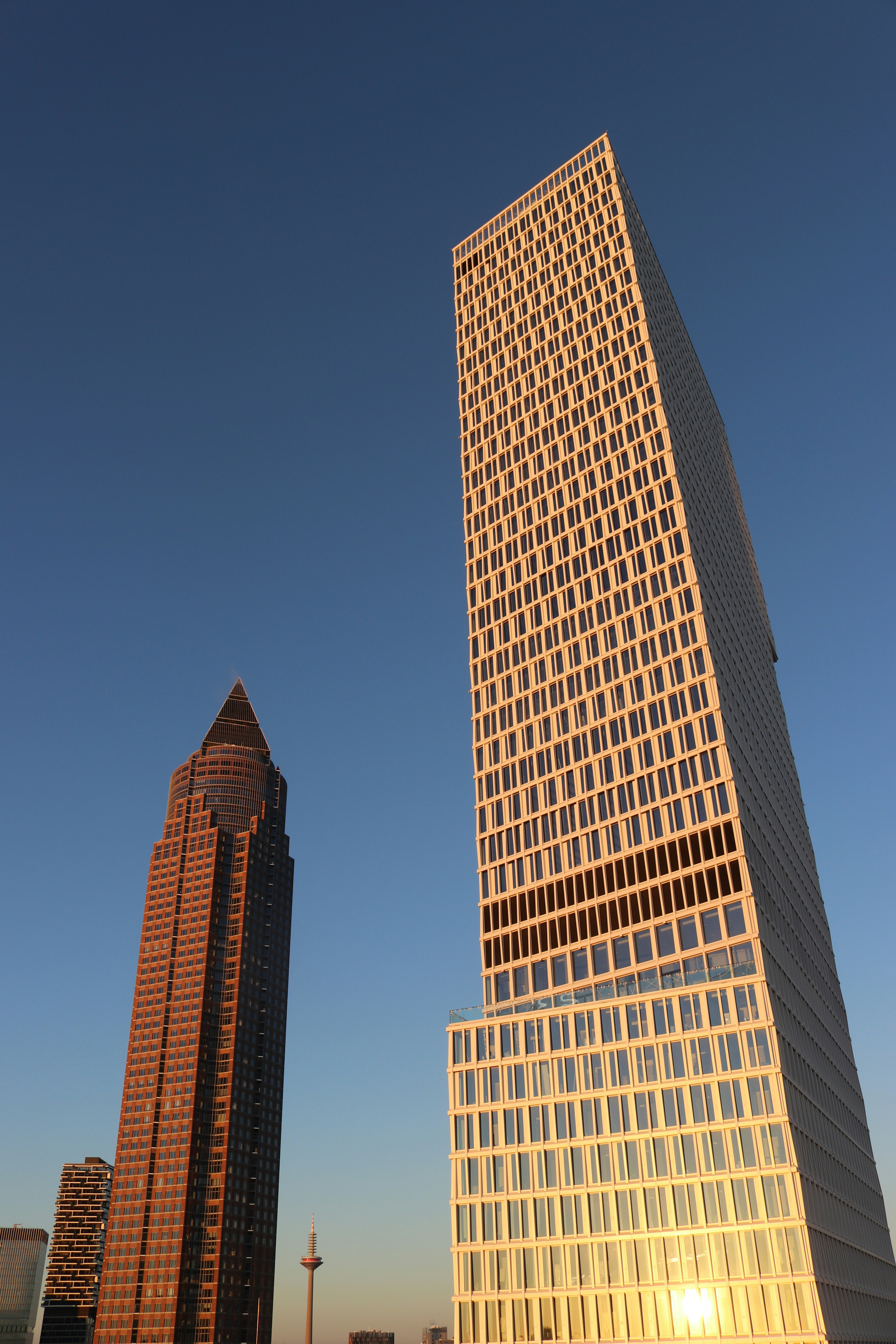 Two skyscrapers stand against a clear sky, with one reflecting the warm hues of sunset. The architectural contrast highlights modern urban design.
