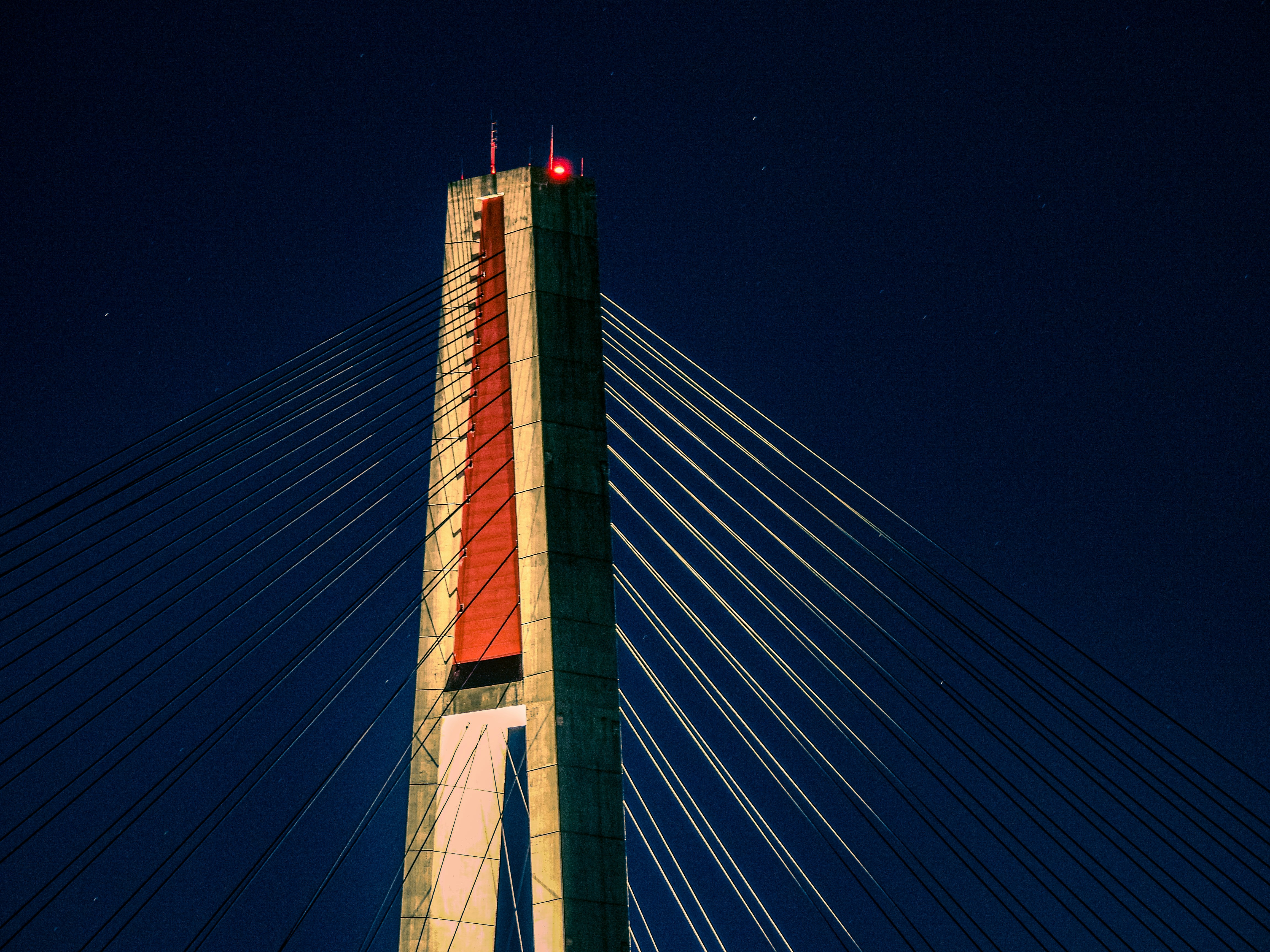 Illuminated bridge tower with red light against a dark night sky, showcasing architectural design and engineering prowess.