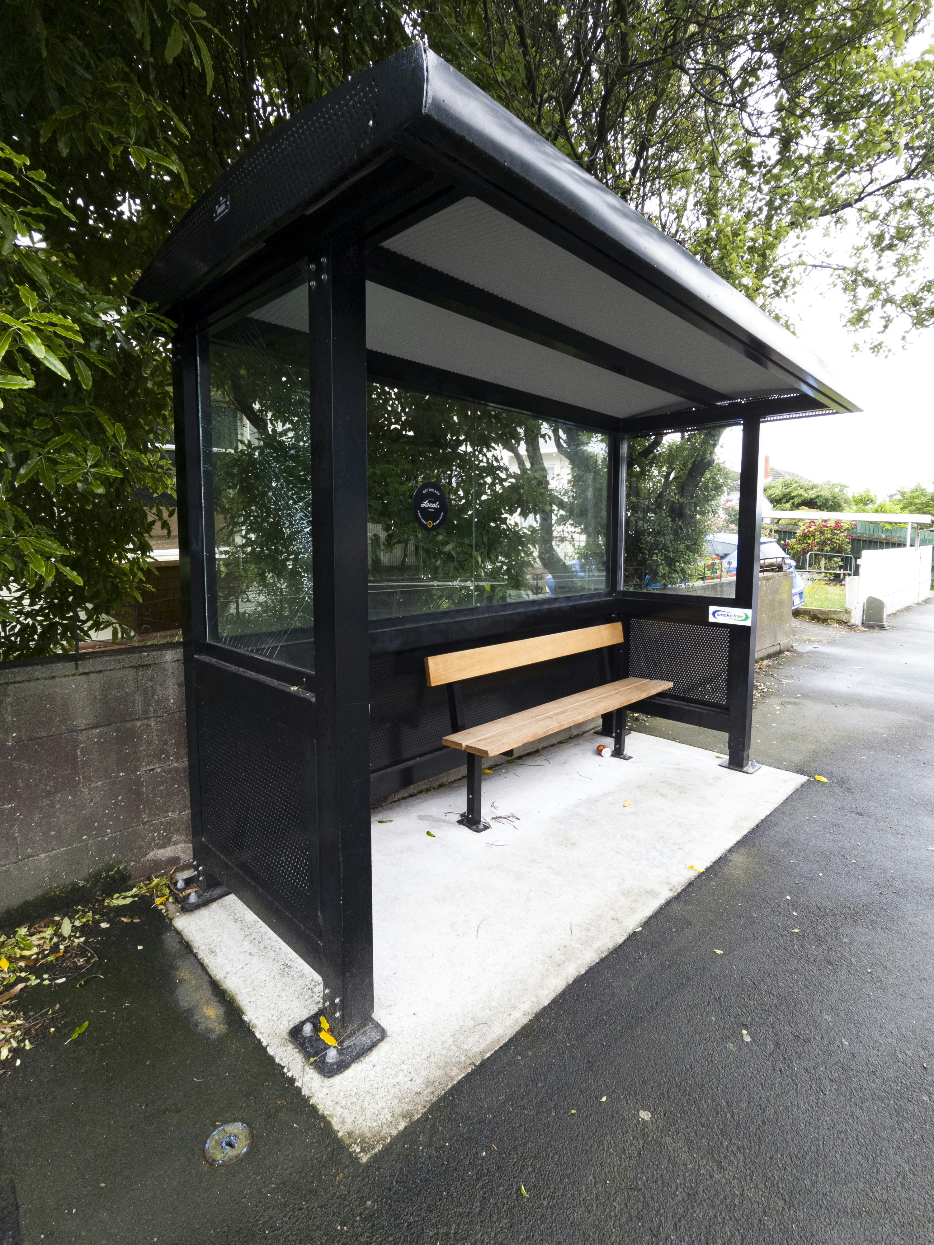 Sleek black bus shelter with a wooden bench, surrounded by lush greenery on a quiet street.
