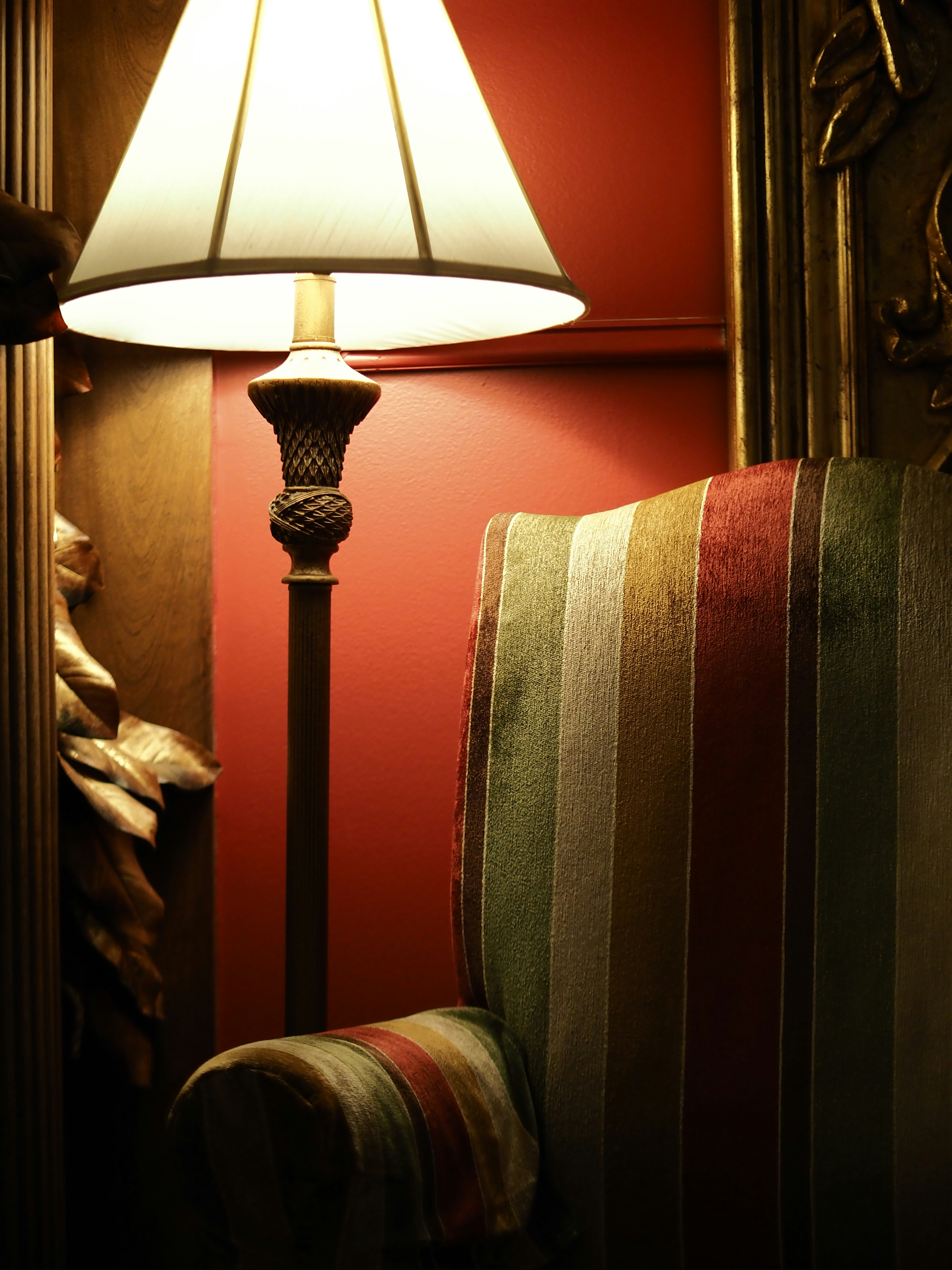 A striped armchair beside a vintage lamp, illuminated against a rich red wall adorned with decorative elements.