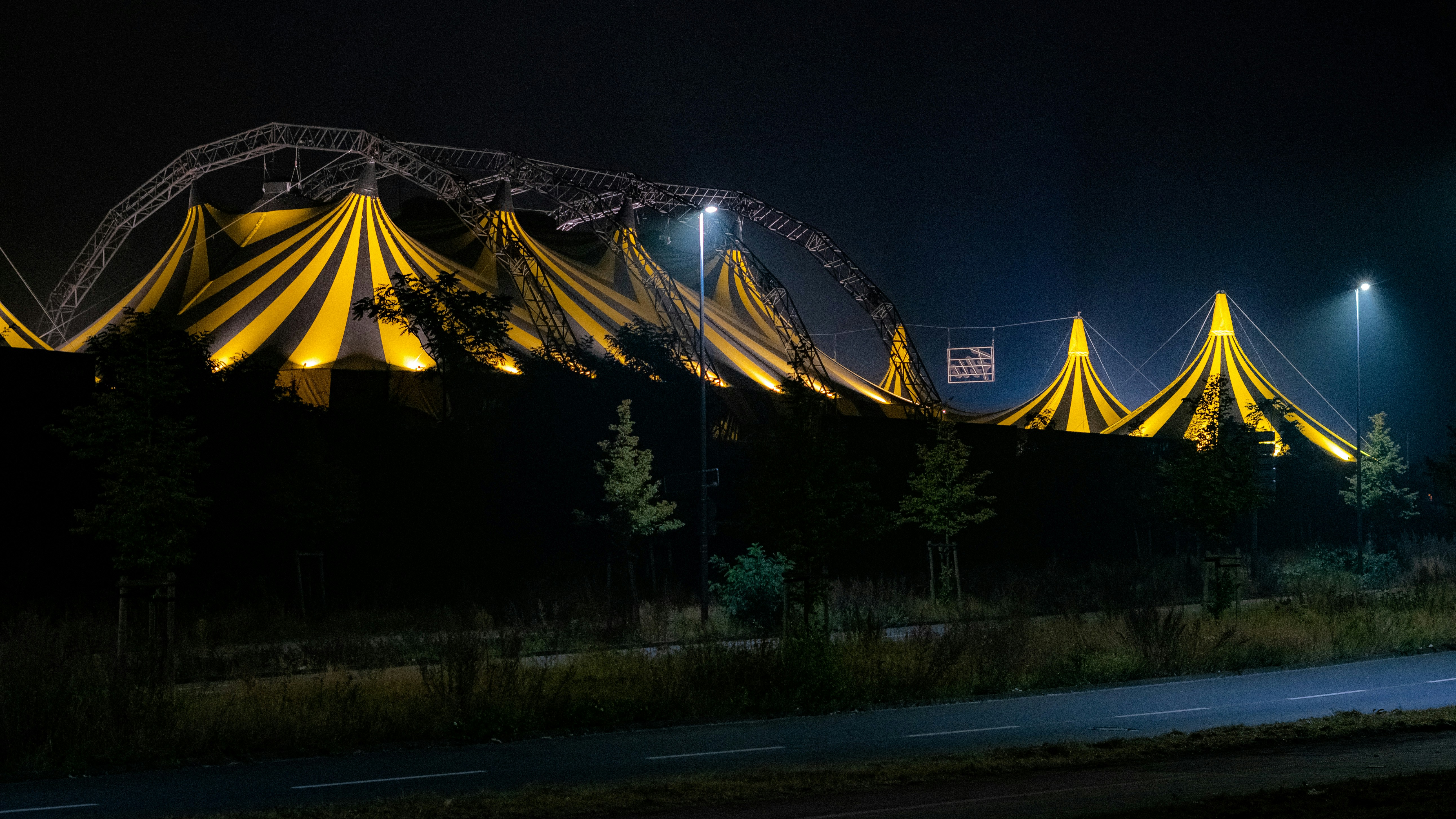 Large circus tent illuminated with yellow lights against a dark night sky.
