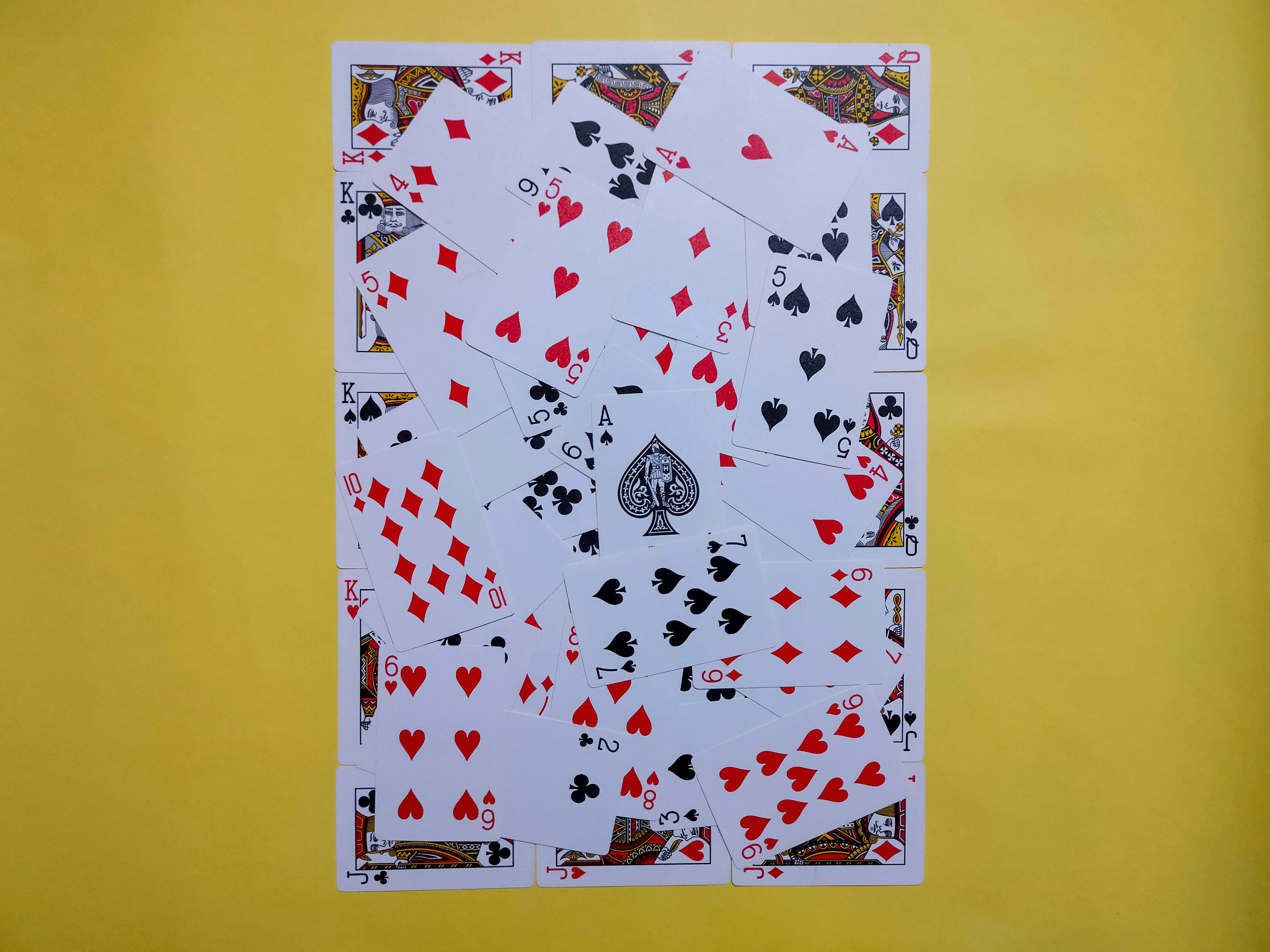 A vibrant arrangement of playing cards scattered across a bright yellow background, showcasing various suits and ranks. The composition emphasizes the randomness of a card game.