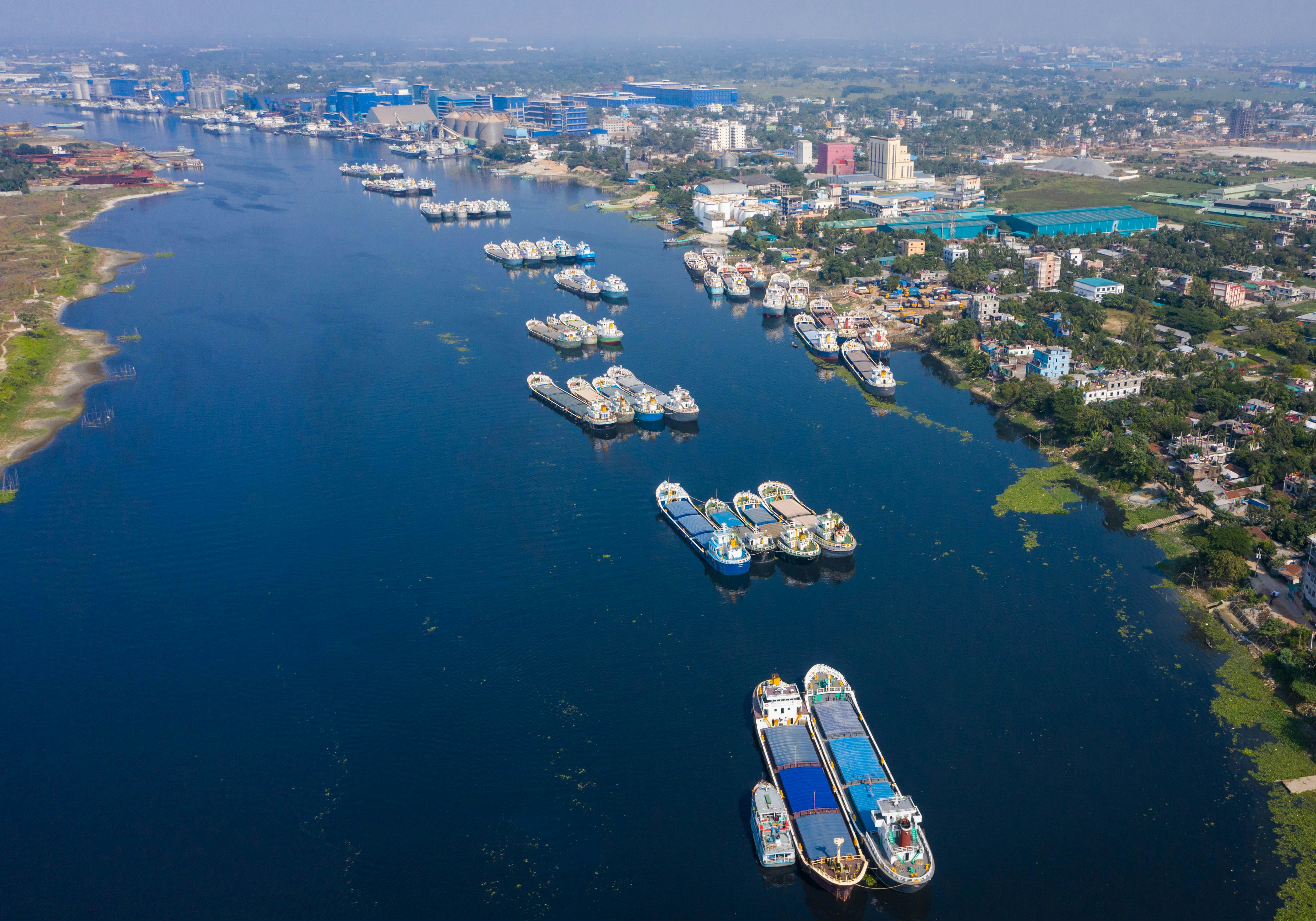 Aerial view of a river bustling with boats, flanked by a sprawling cityscape under a clear sky.