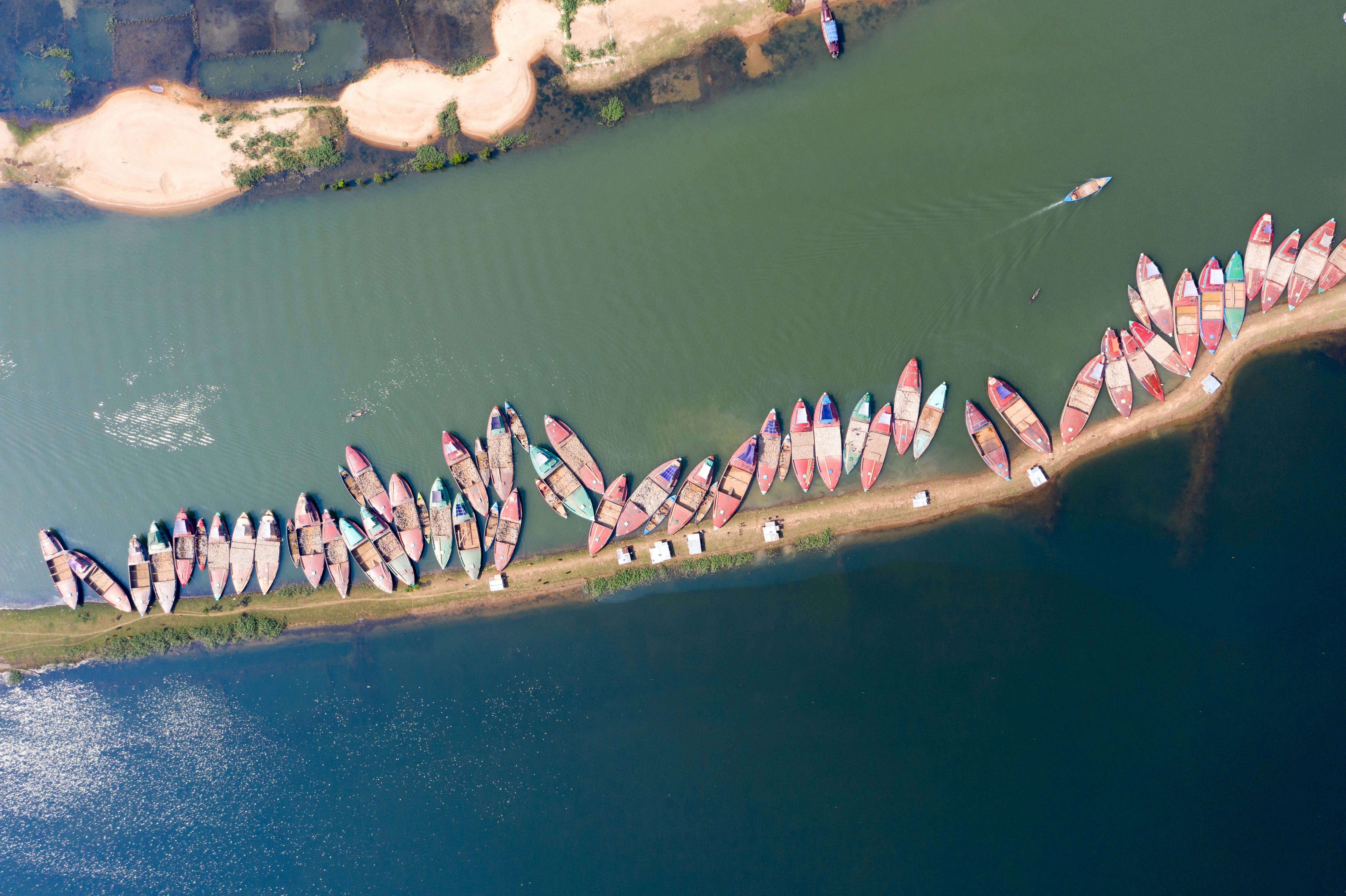 Lines of boats along a sunlit riverbank from above