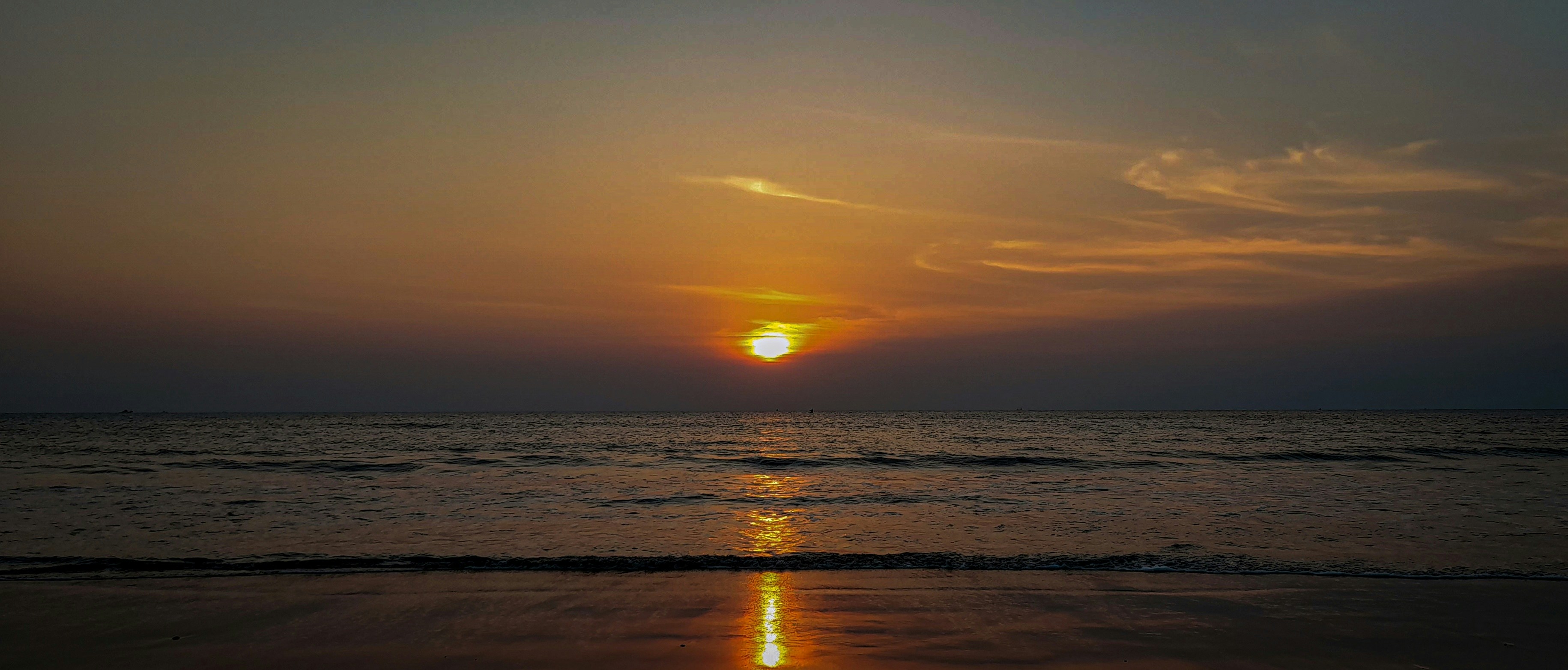 Golden sun dipping below the horizon, casting reflections on calm ocean waters at dusk.
