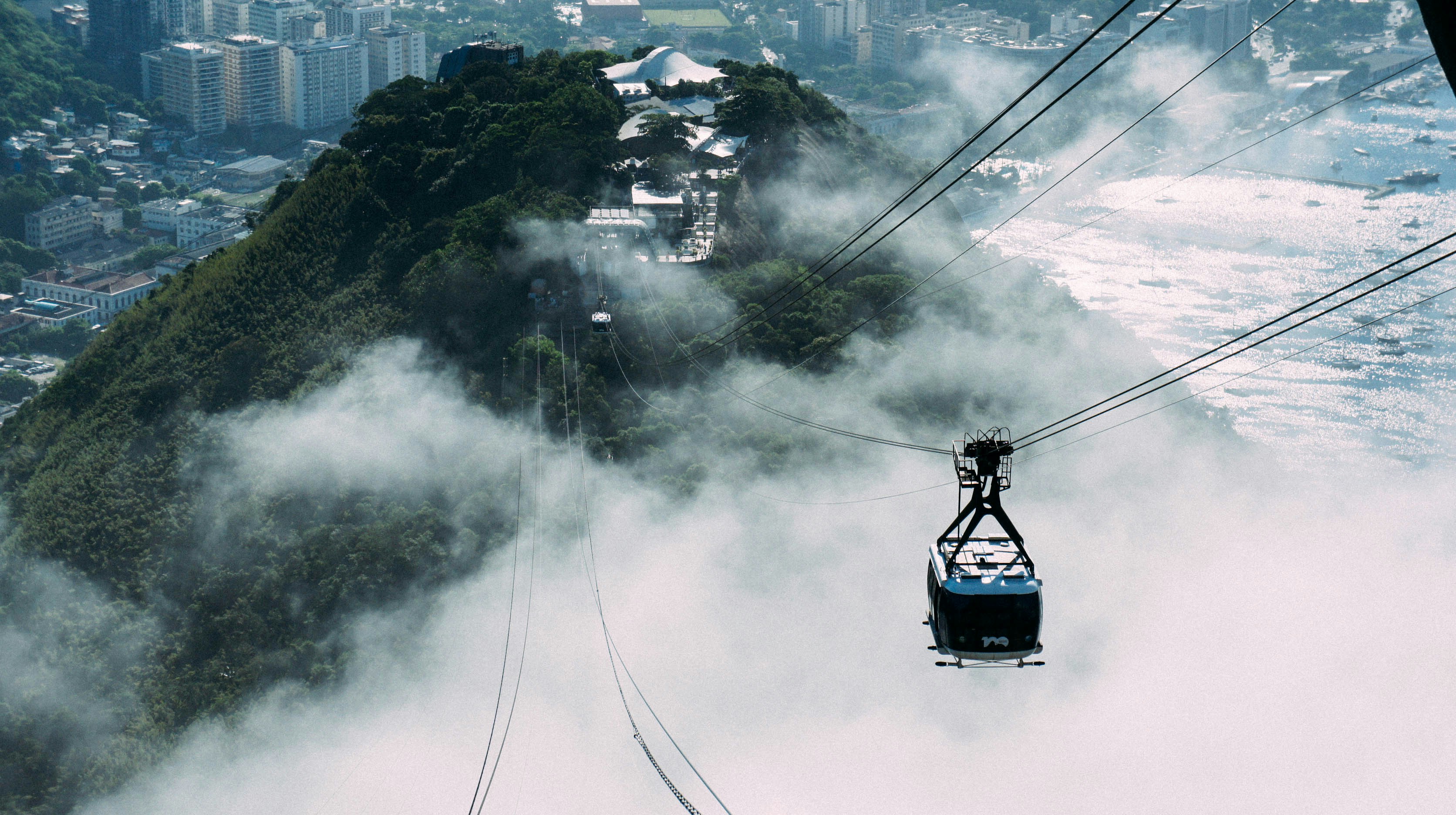 A cable car glides through misty clouds, revealing a mountainous landscape and distant city skyline. The scene captures the serene beauty of elevated travel.