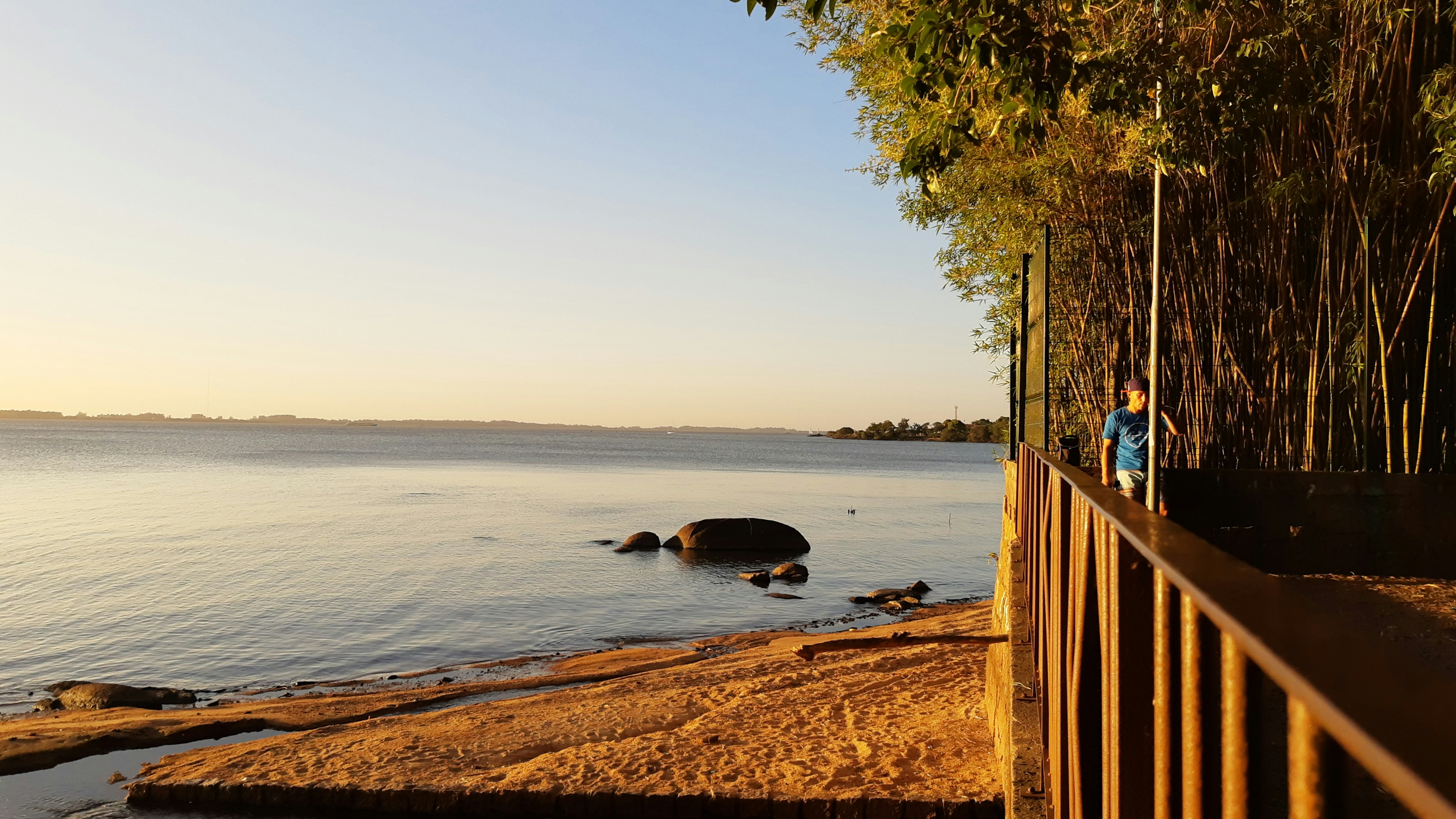Calm lake waters beside a wooden fence under a clear sky at dawn.