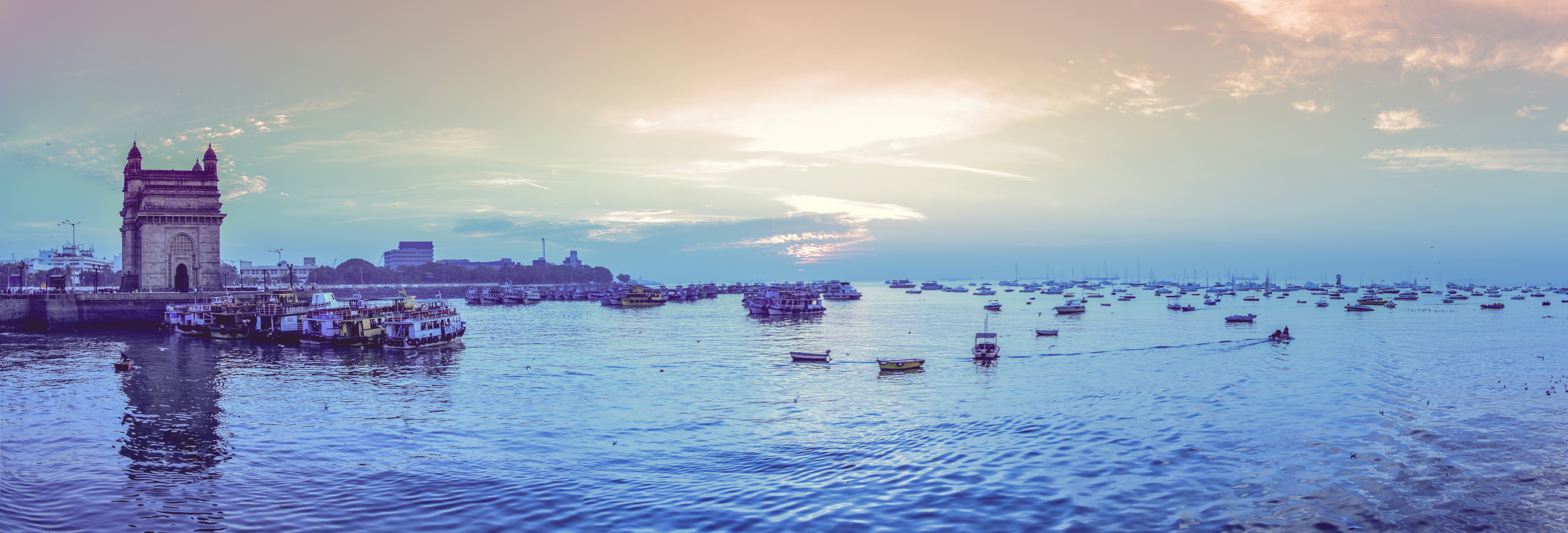 Panoramic view of the Gateway of India with boats scattered across the tranquil waters during twilight.