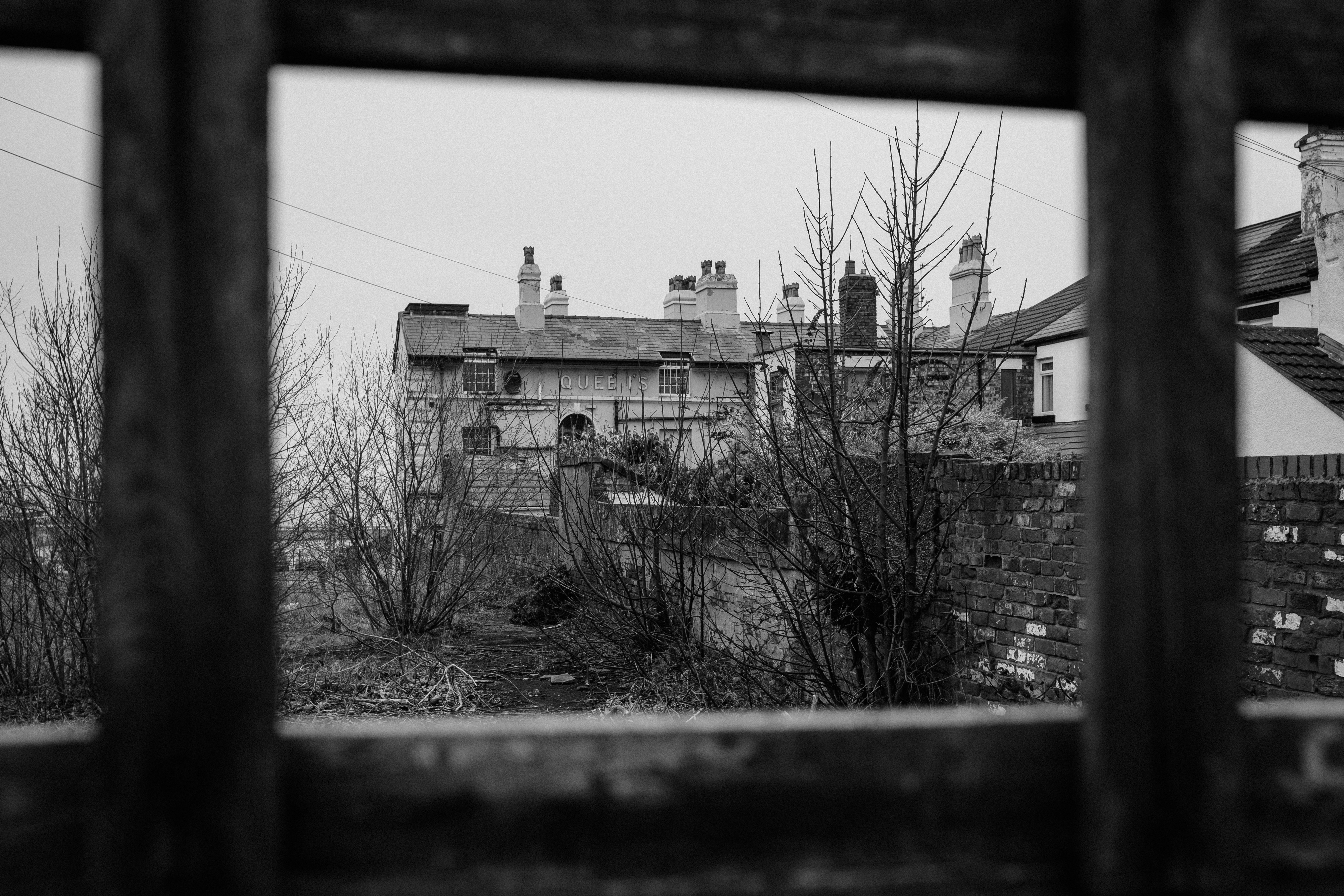 Monochrome view of old stone buildings seen through a wooden fence in a desolate landscape.