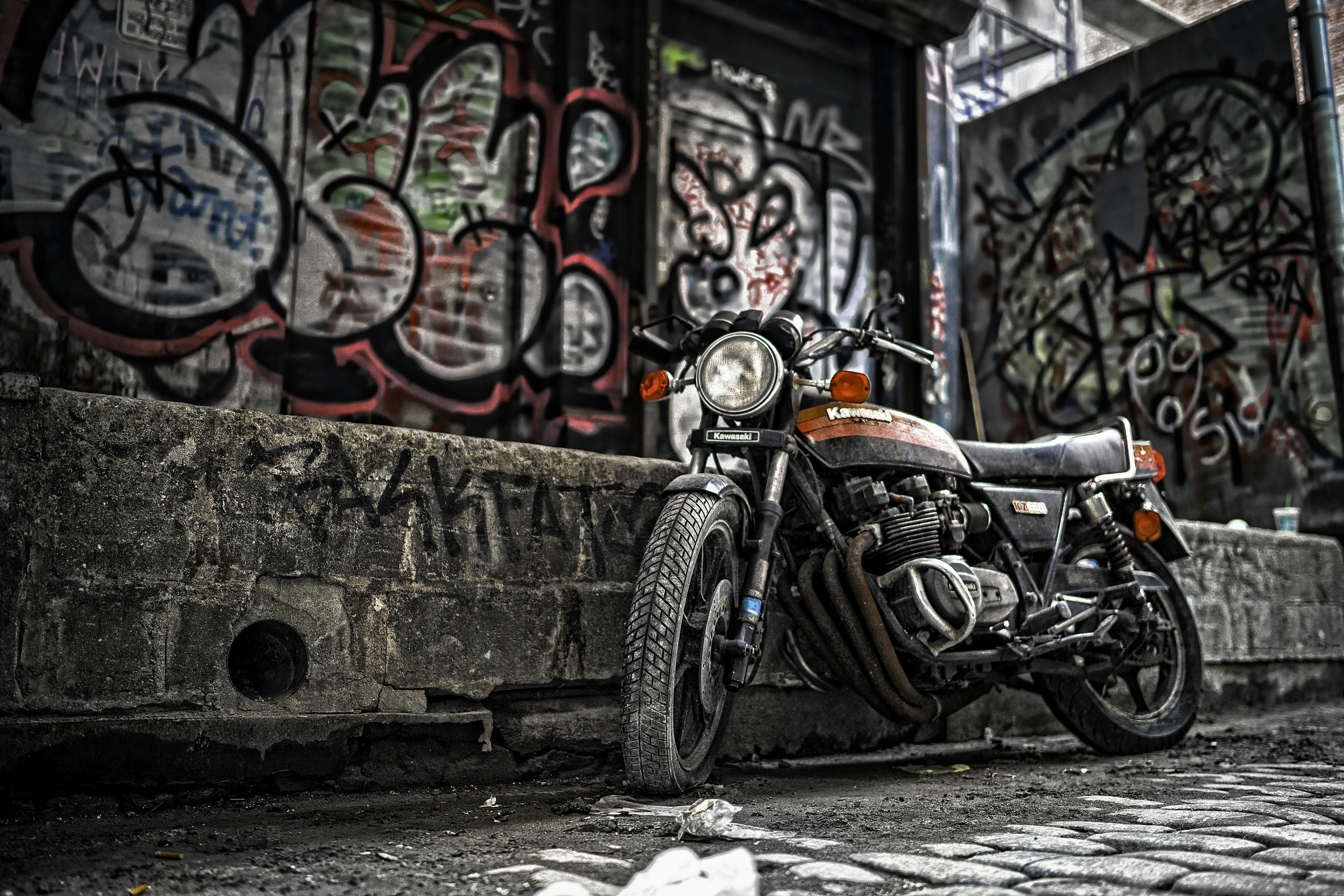 Abandoned motorcycle resting against a graffiti-covered wall in an urban alleyway, showcasing the contrast between decay and vibrant street art.
