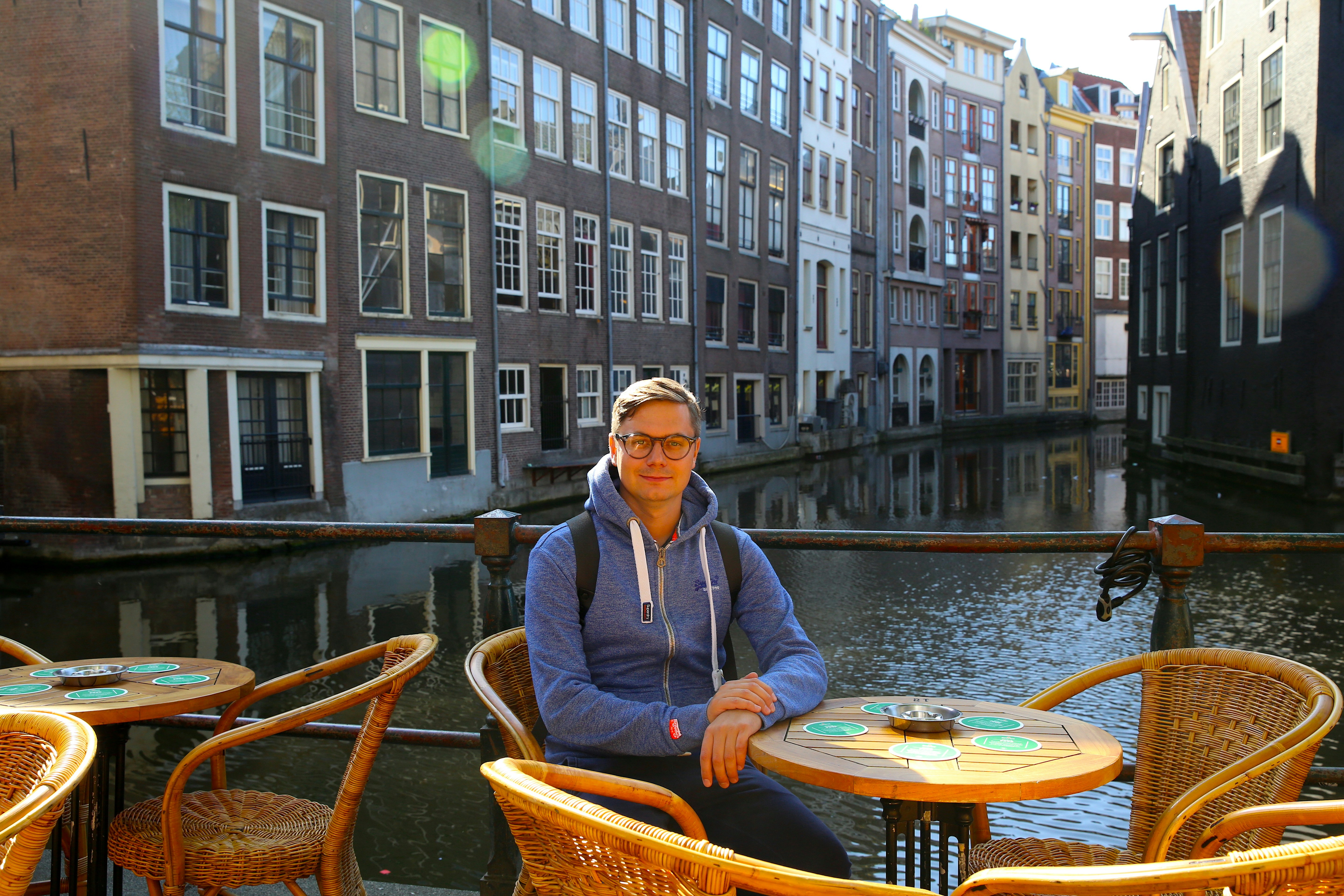 A relaxed individual seated at a café table beside a serene canal, surrounded by historic buildings reflecting in the water.