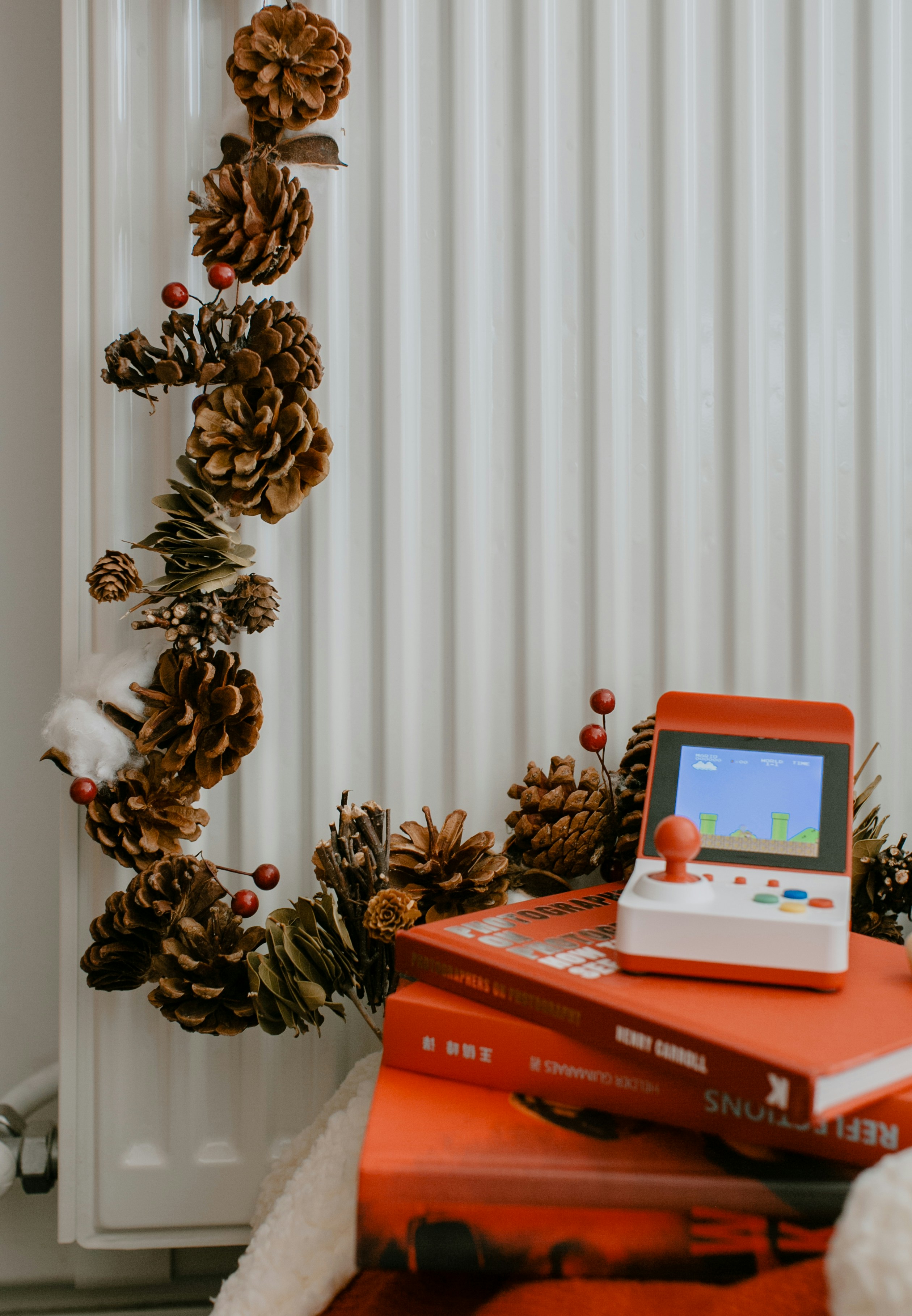 Crimson Volumes and Pinecone Accents: A Cozy Still-Life with a Retro Handheld Console