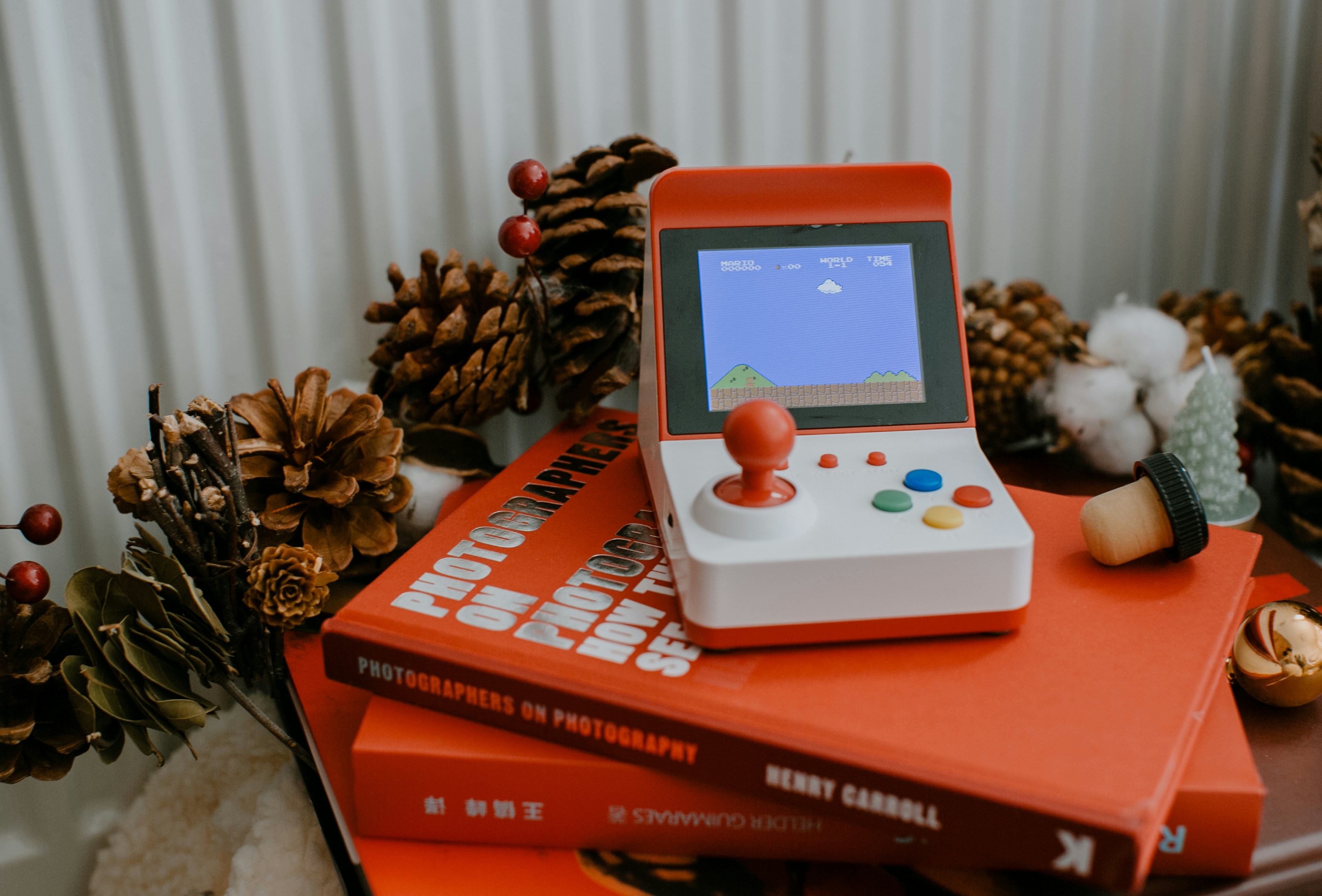 Tiny Retro Console resting on a stack of photography books amid pinecones and holiday décor